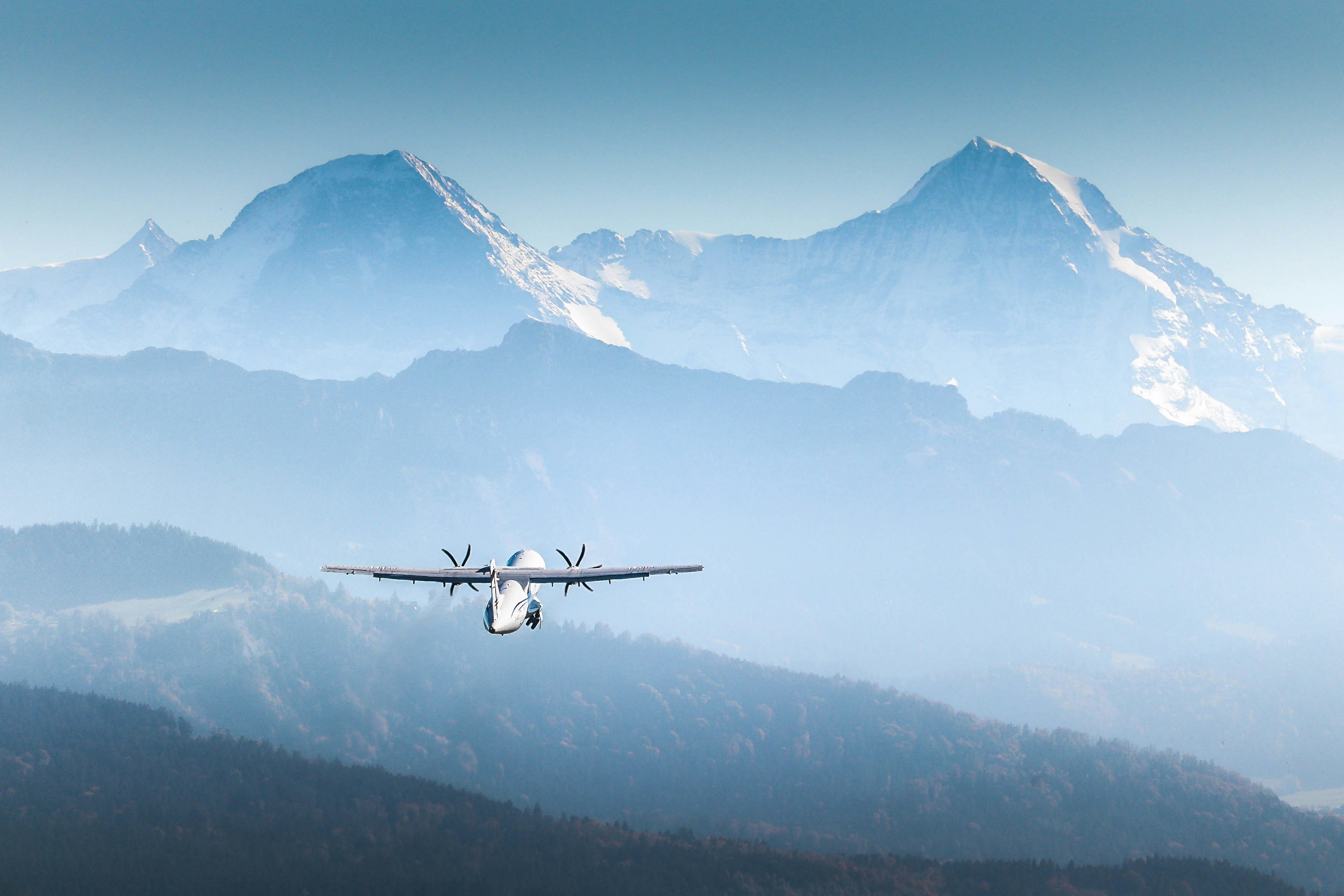 Small aircraft flying towards distant snow-capped mountains under a clear blue sky.