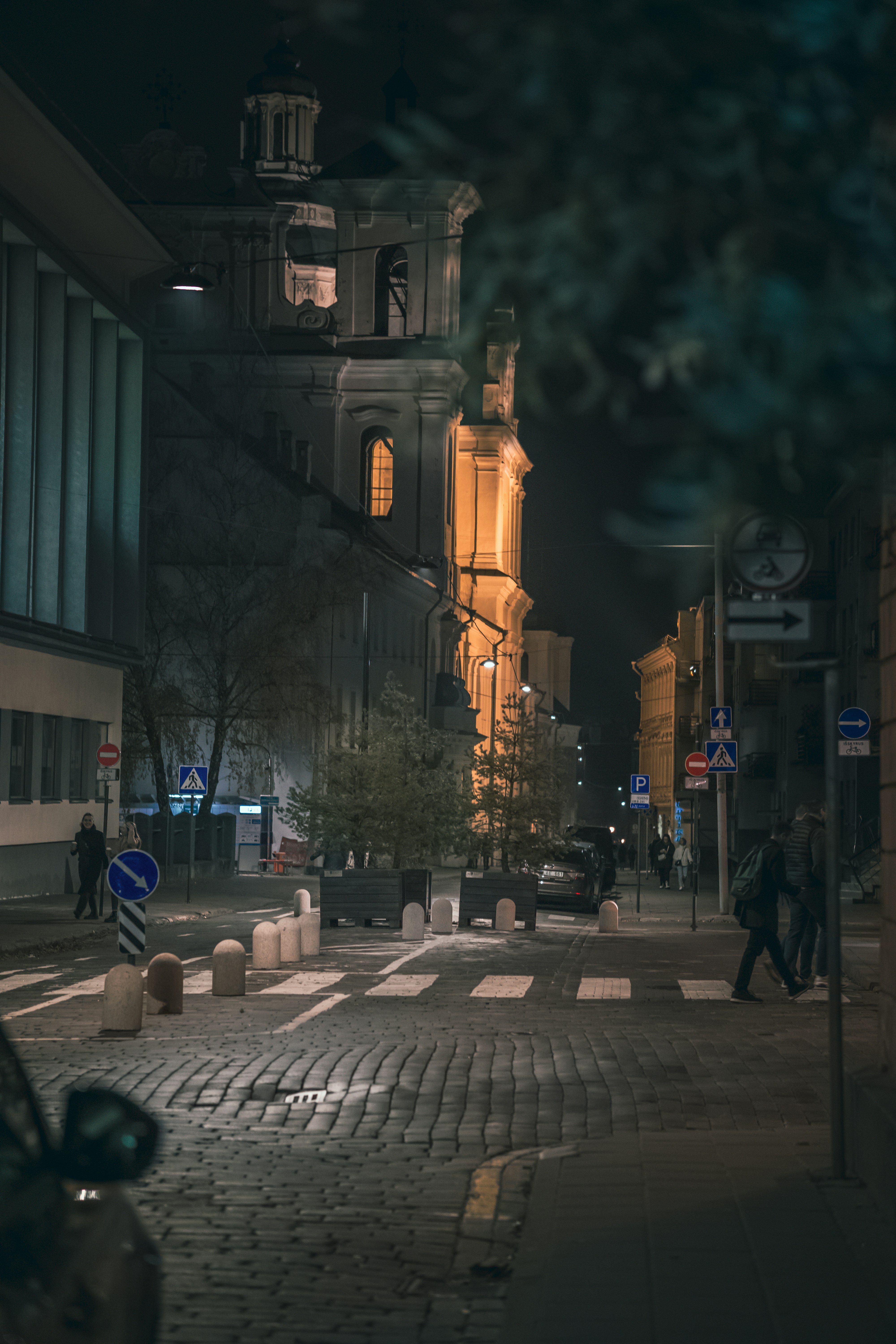 Historic building illuminated at night, casting warm light on cobblestone street, with pedestrians walking by.