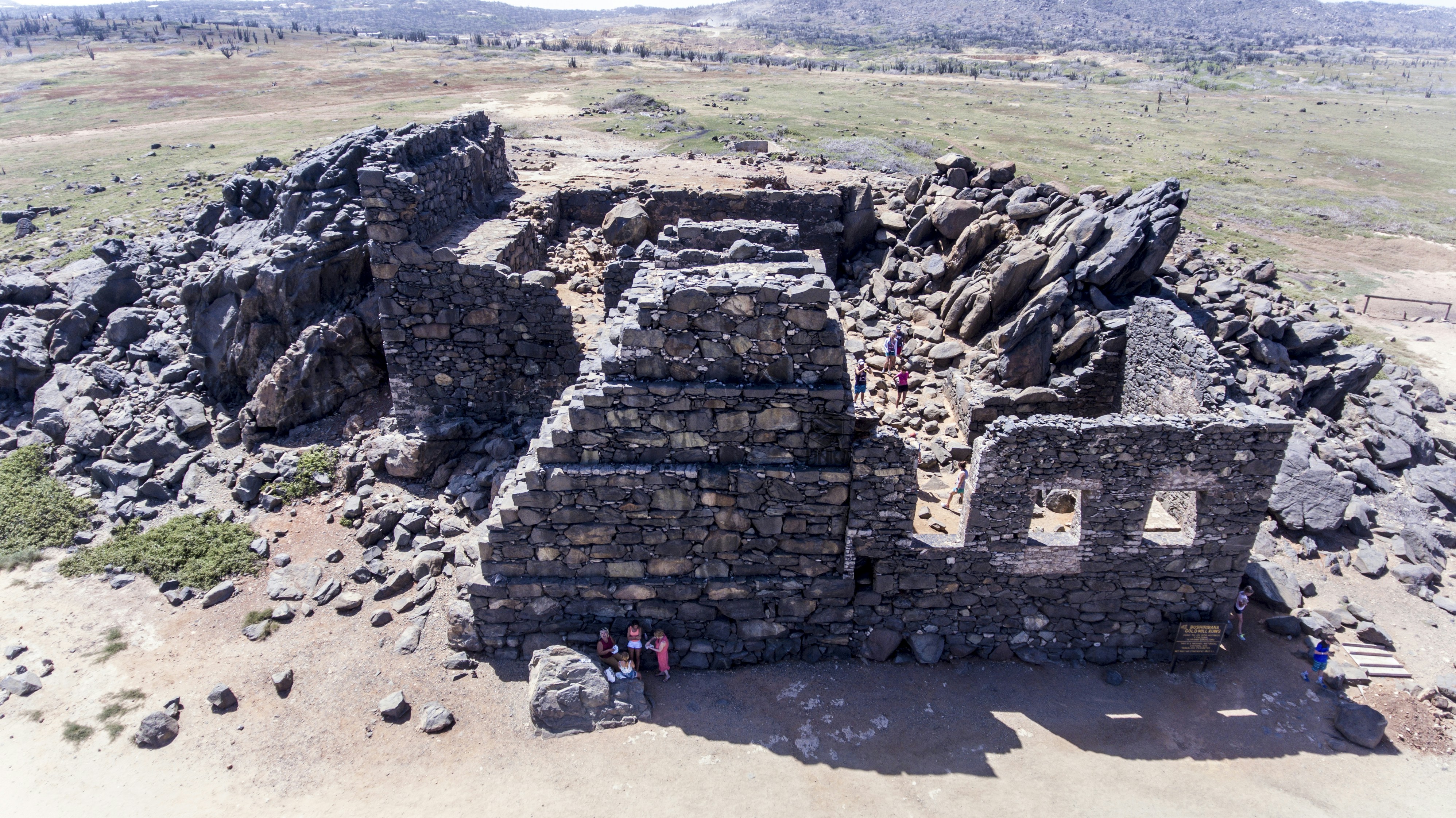 Ancient stone ruins nestled among rugged terrain, showcasing remnants of a bygone civilization. Visitors explore the historical site under a clear sky.