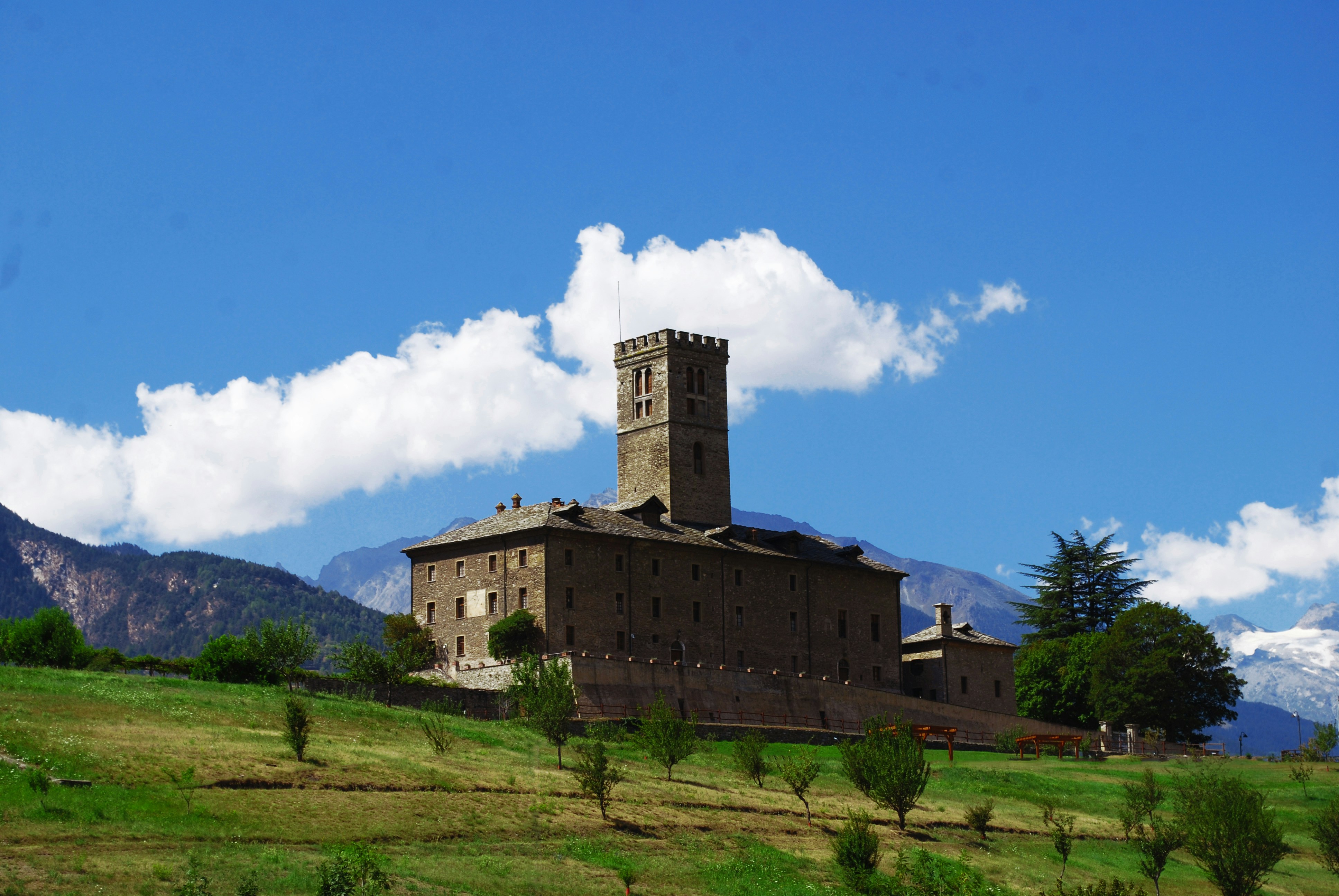 Historic stone tower rising above a lush green landscape with distant mountains under a clear blue sky.
