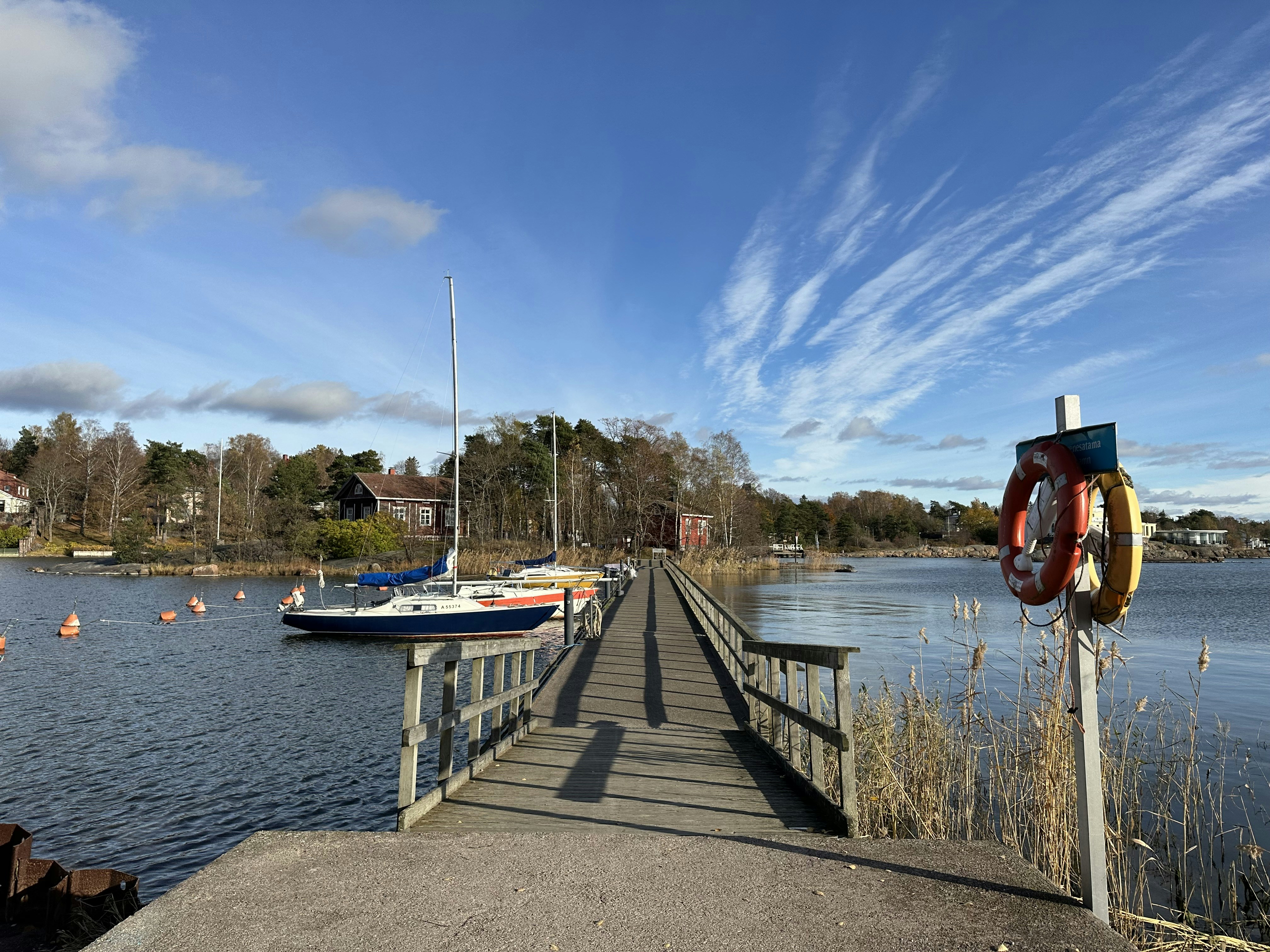 Pier to the Horizon: Boats, Lifebuoy, and a Bright Blue Sky