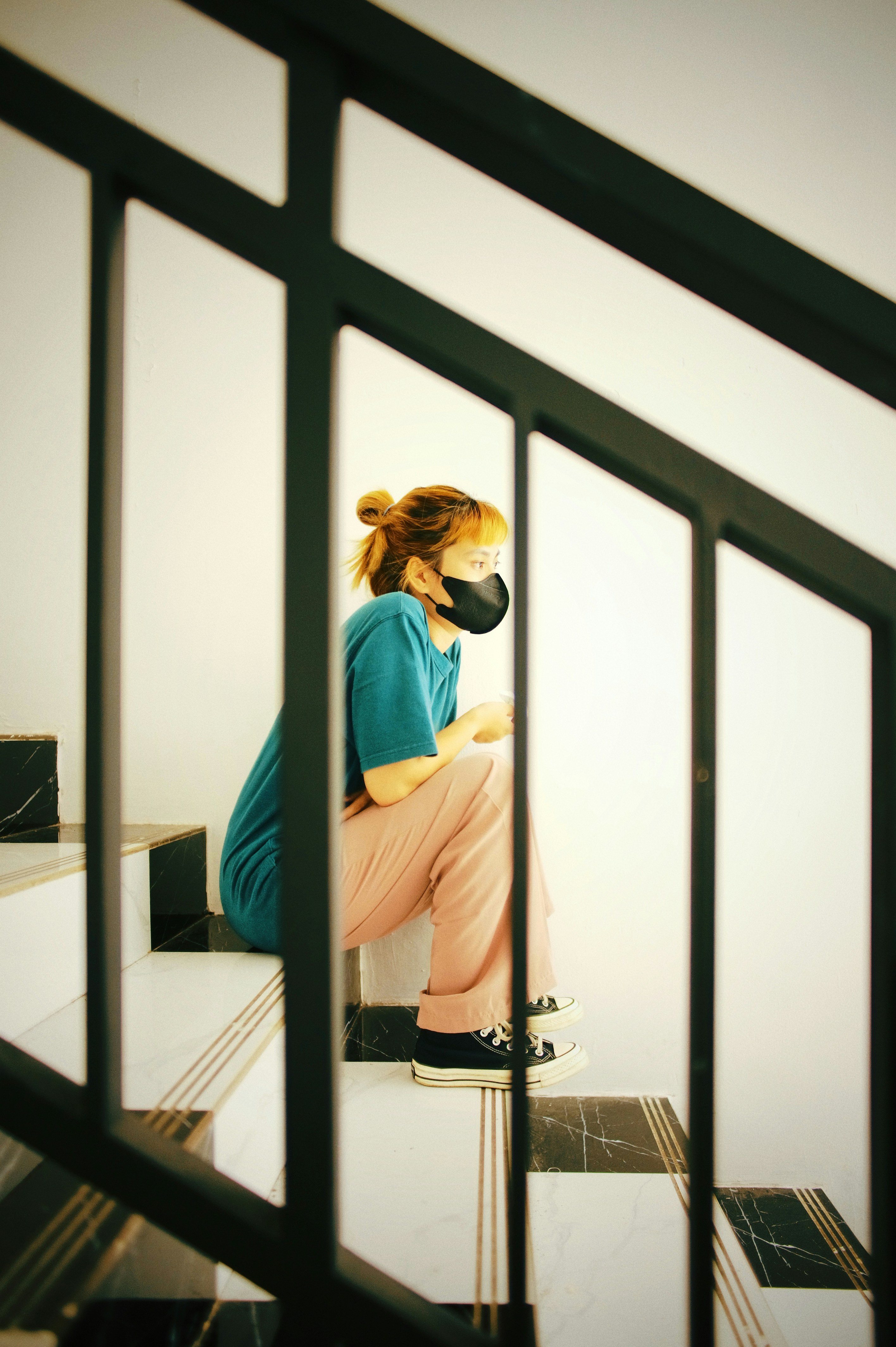 Masked Quiet on the Stair: A Candid Moment Through a Framed Railing