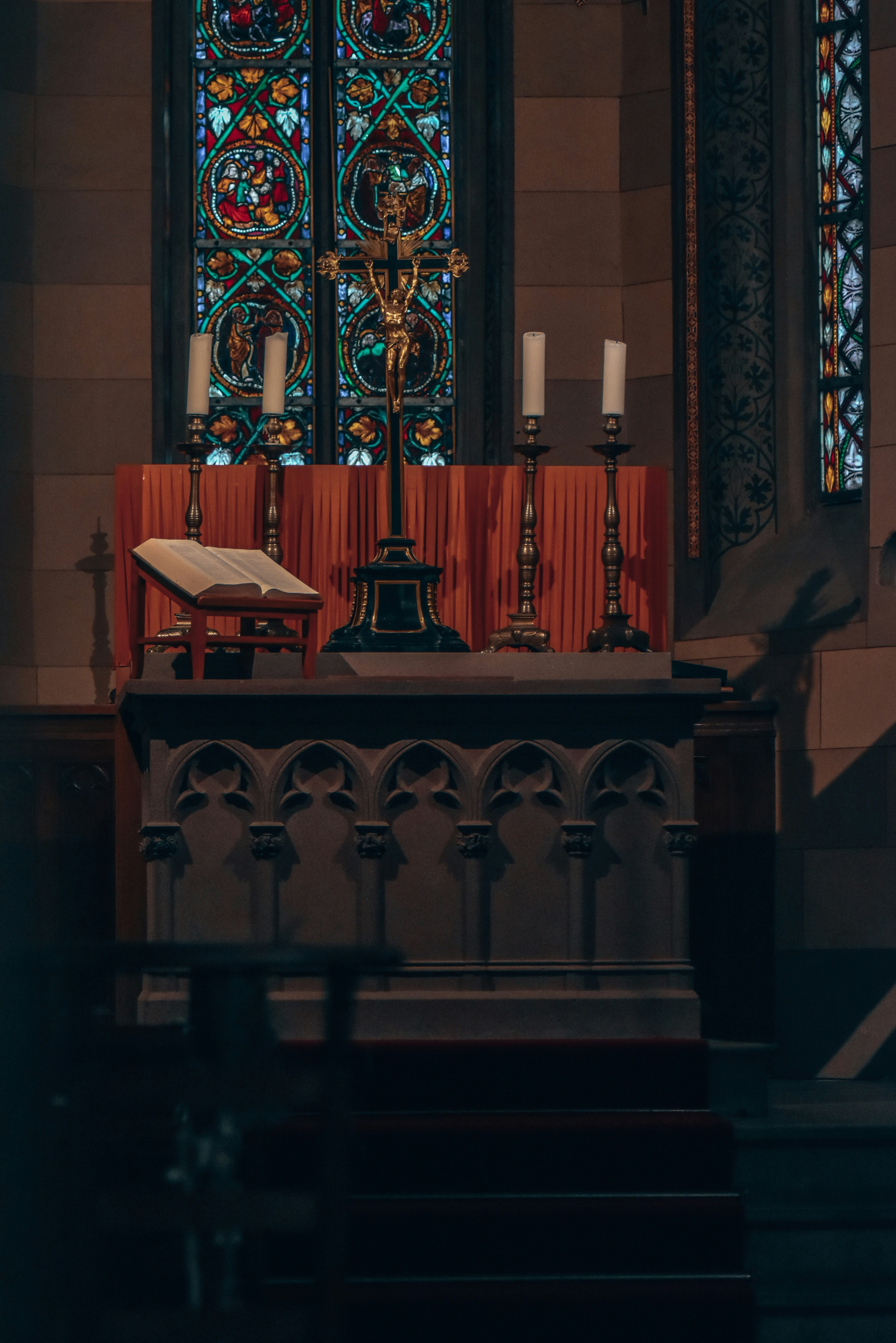 Altar adorned with candles and a crucifix, framed by vibrant stained glass windows in a quiet church setting.