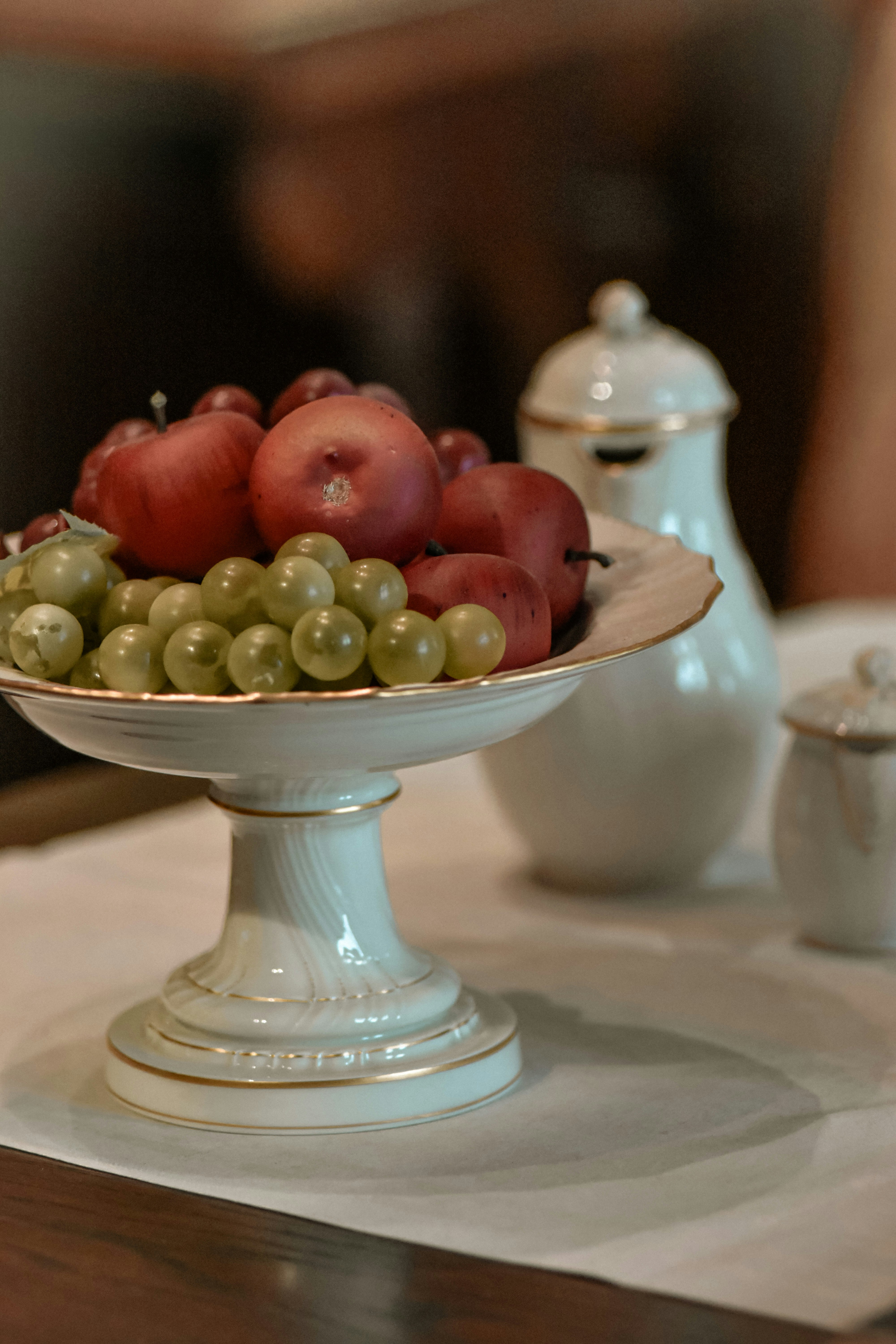 Gilded Still Life: Apples and Green Grapes on a White Ceramic Pedestal