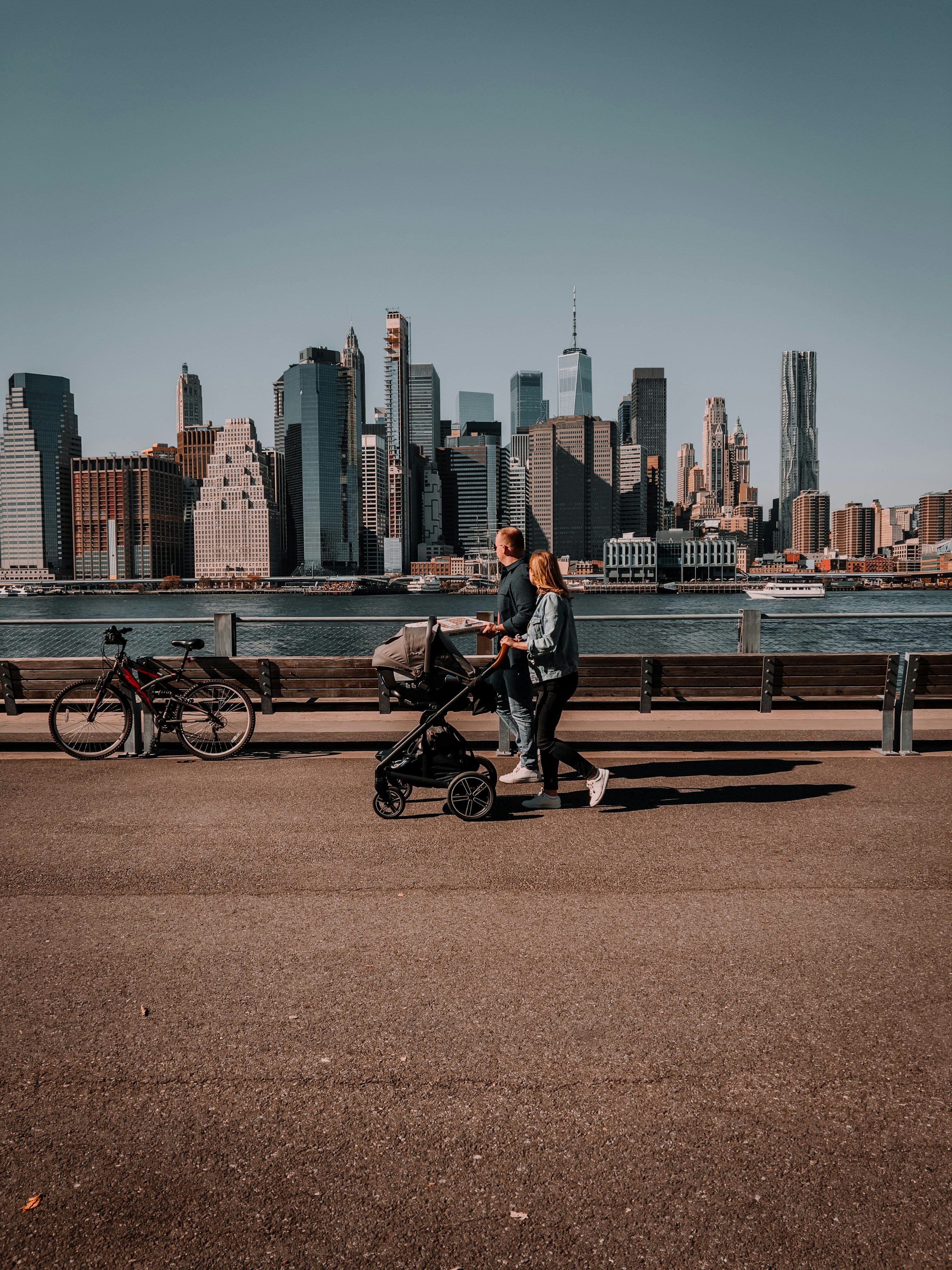 a man and woman walking with a stroller by a body of water