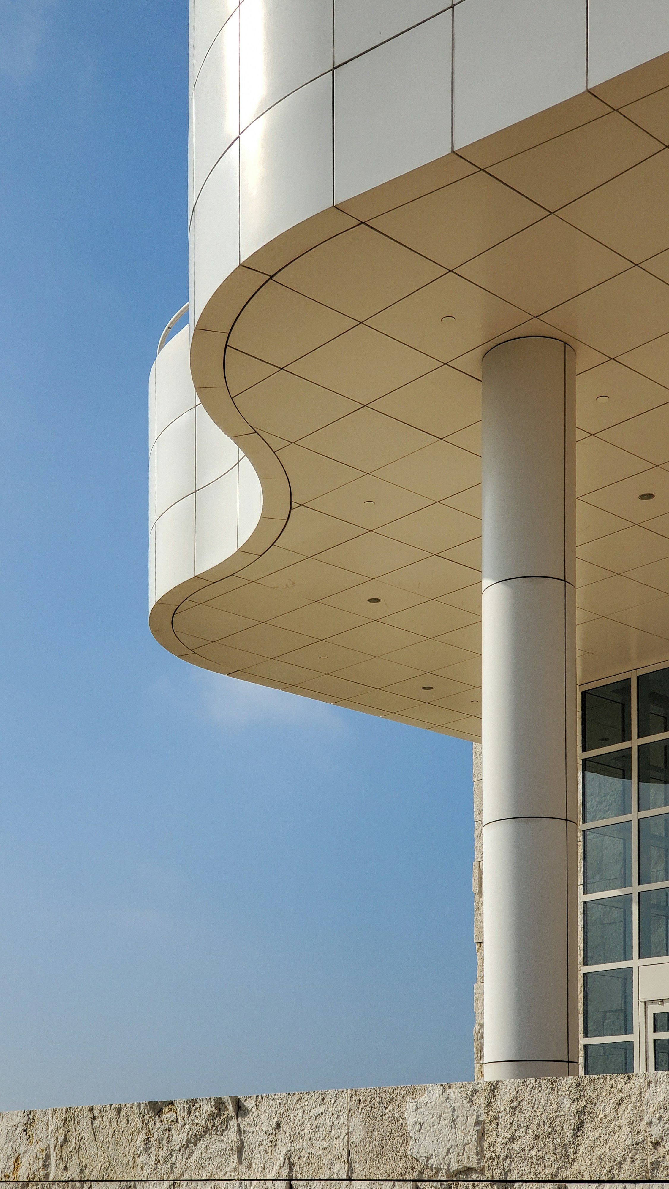Architectural photograph of a white curved facade supported by a cylindrical pillar against a clear blue sky.