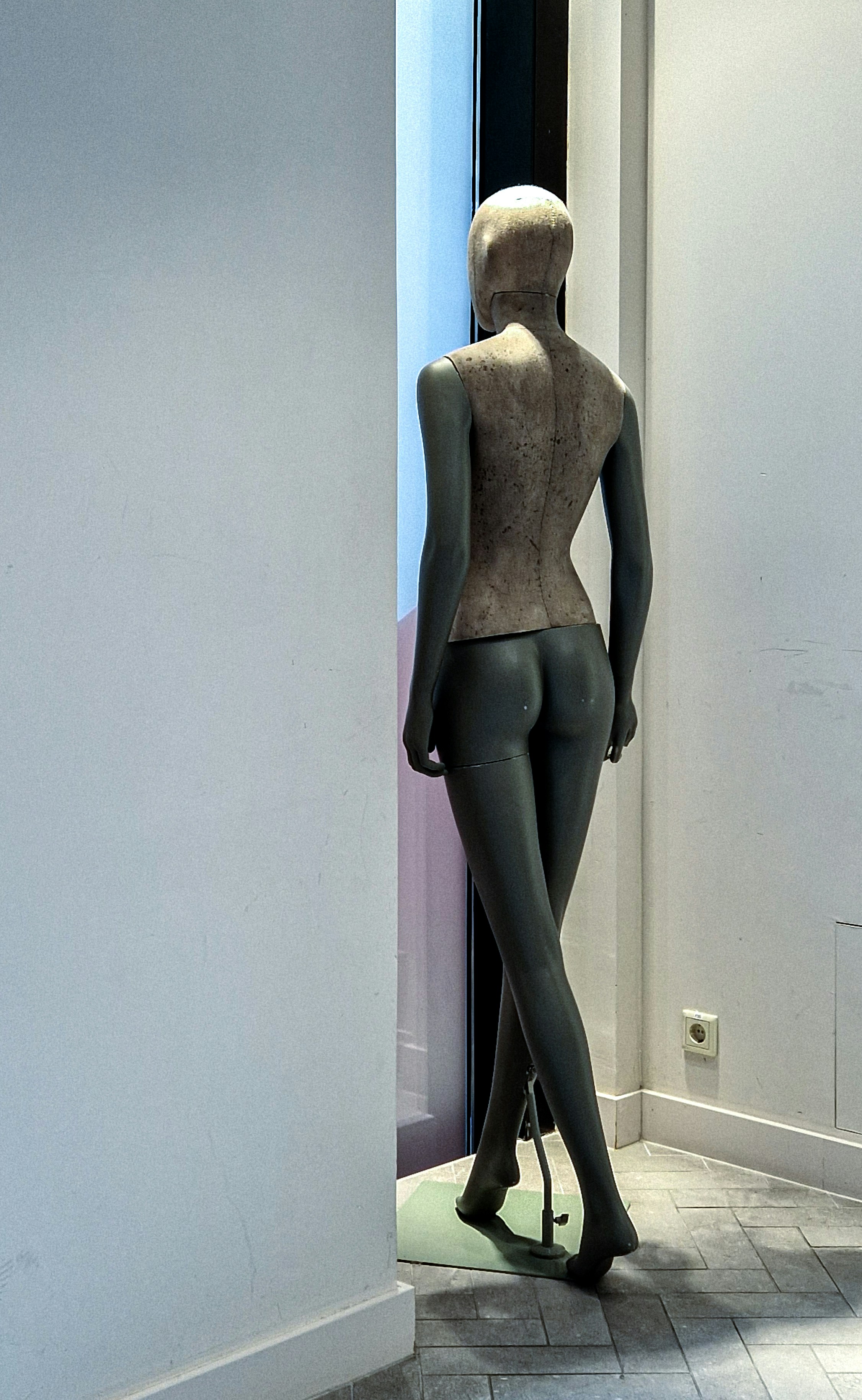 Mannequin poised in a corner, casting soft shadows on a tiled floor.