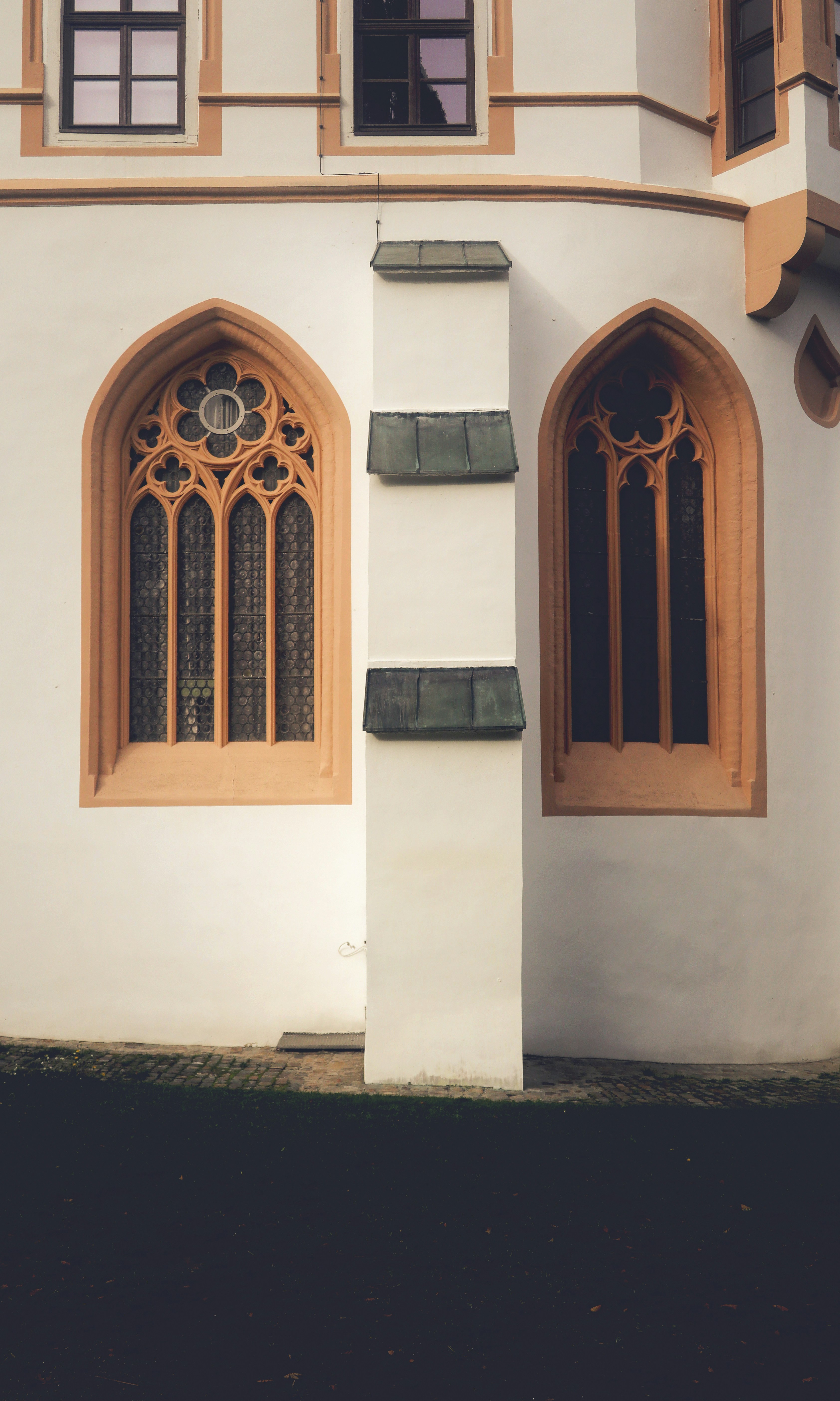 Gothic-style windows with intricate stone detailing on a sunlit white wall.