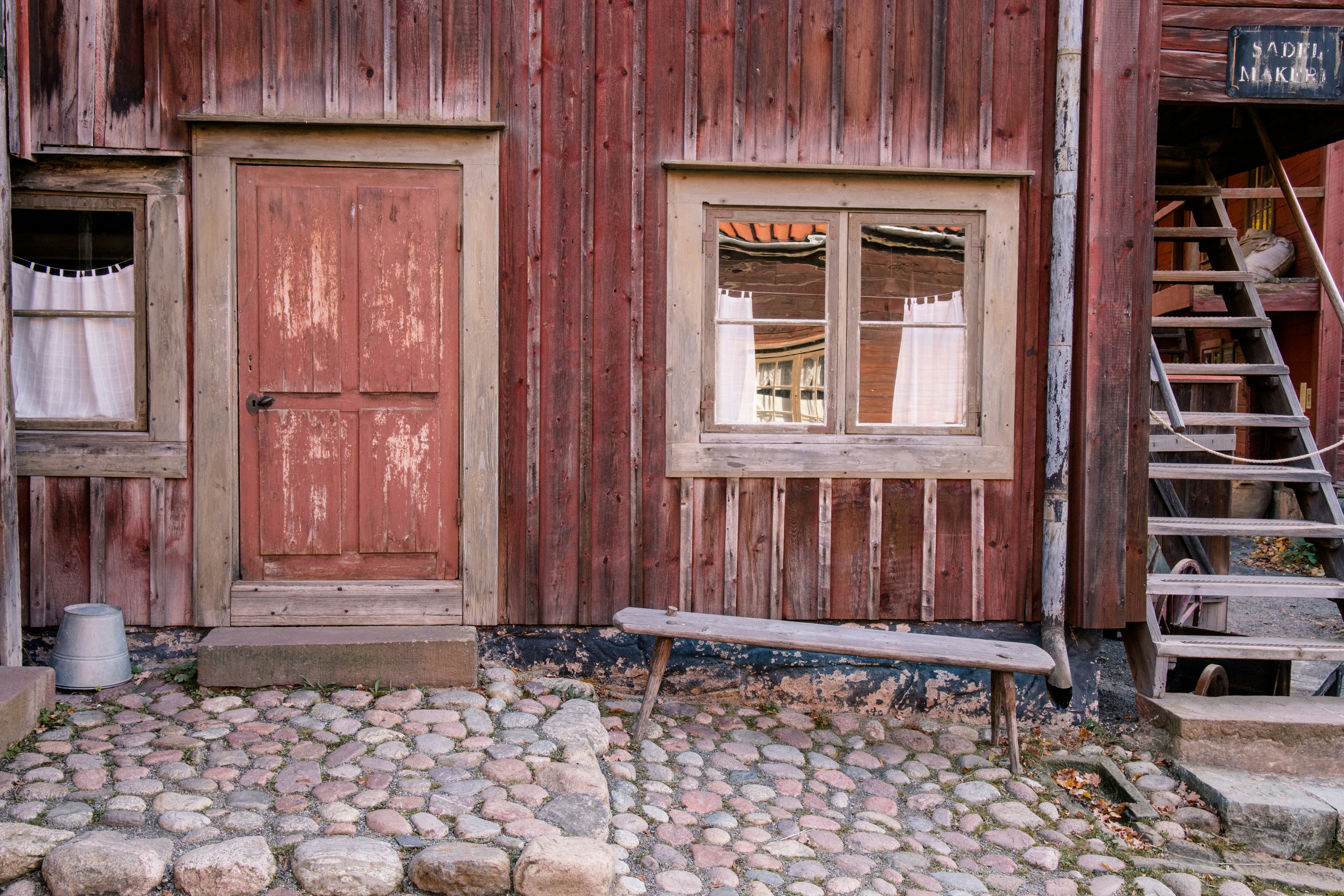 Rust-Red Barn Facade: Windowed Gaze Over a Cobblestone Path