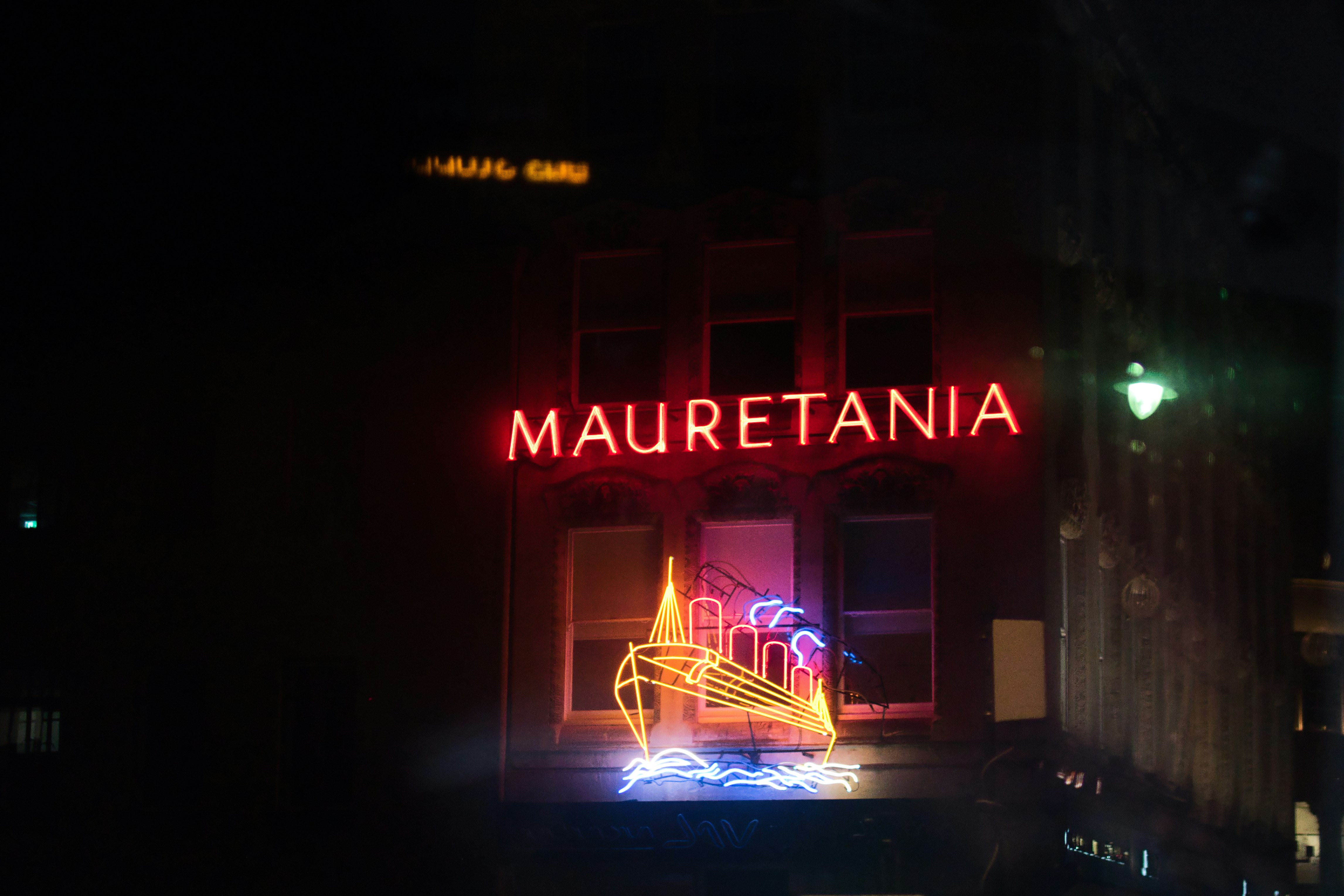Neon lights illuminate a building facade with the word 'Mauretania' glowing in vivid red at night.