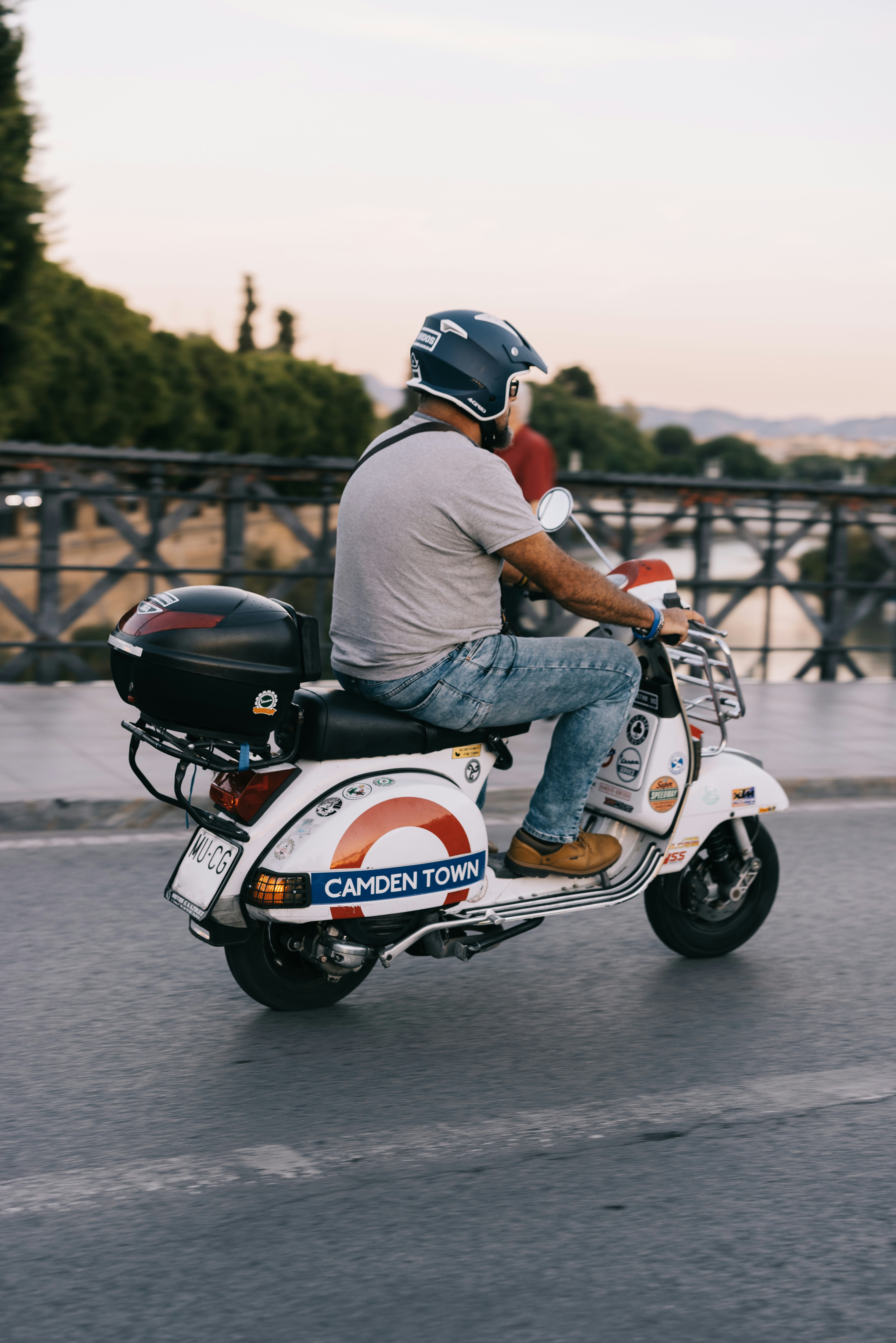 Man on a retro scooter rides along a city street at dusk.