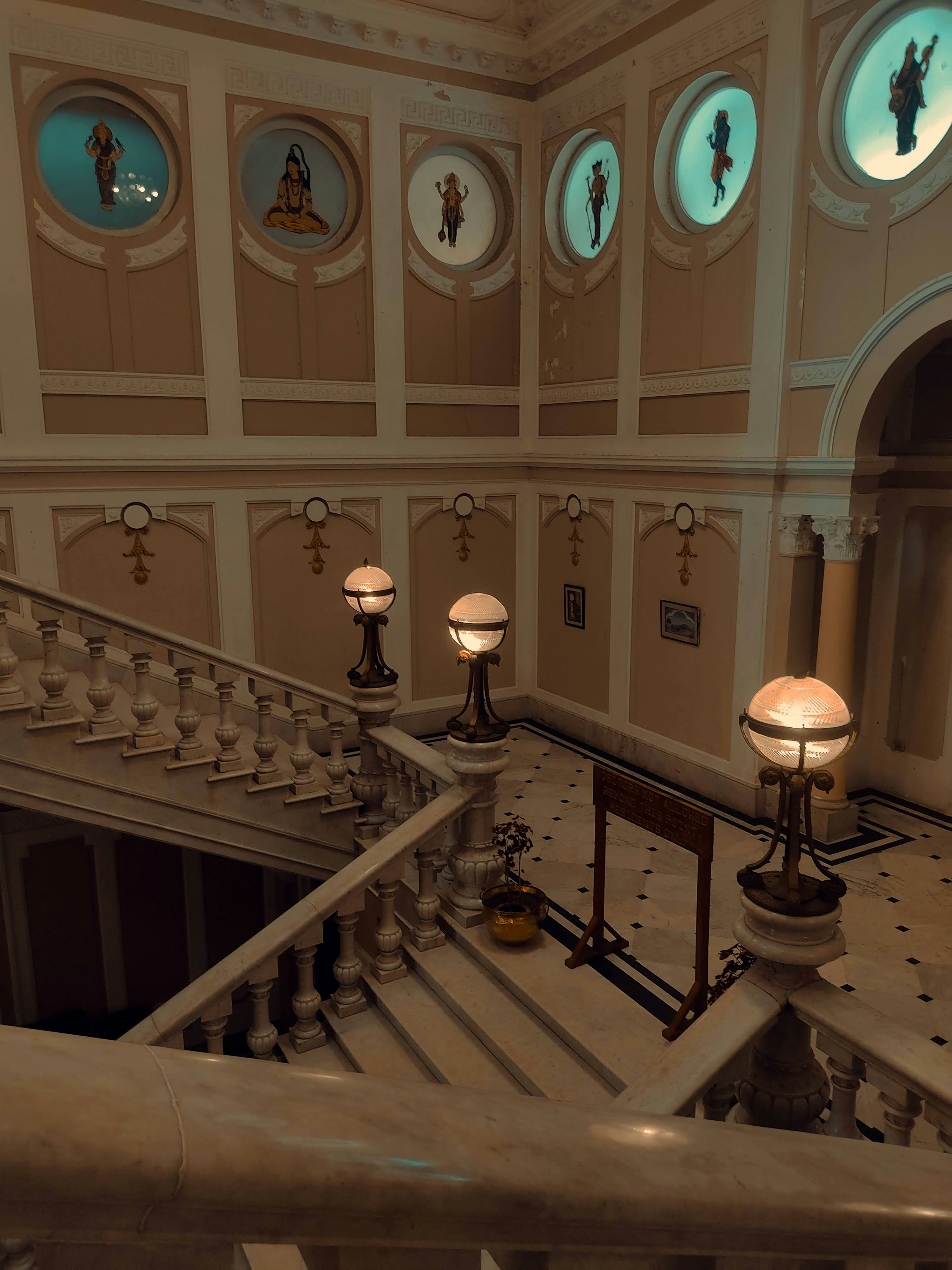 Intricate staircase illuminated by vintage lamps, featuring decorative wall art in a historic building.