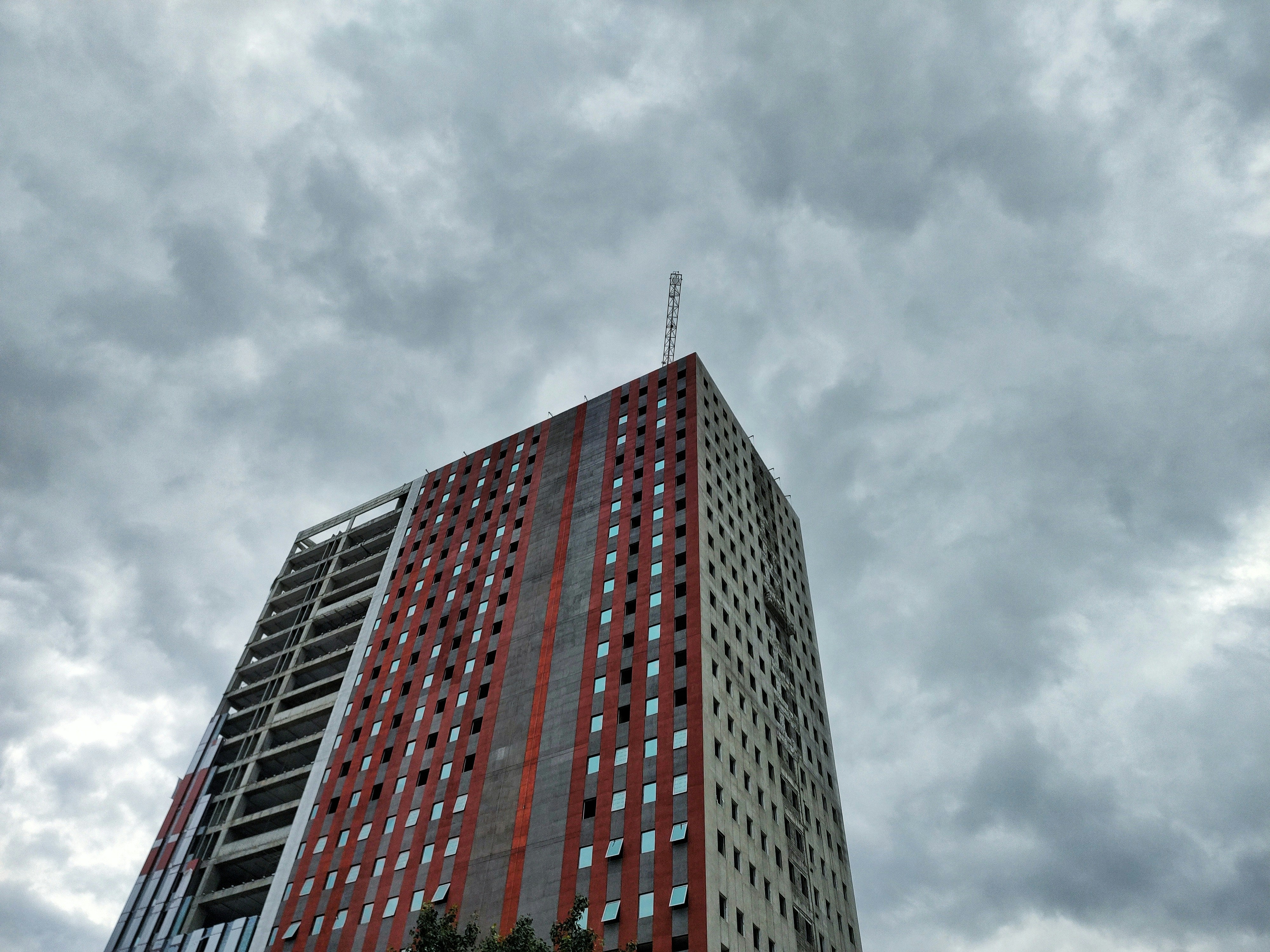 A tall building with a striking red and gray facade rises against a cloudy sky, showcasing contemporary urban design.