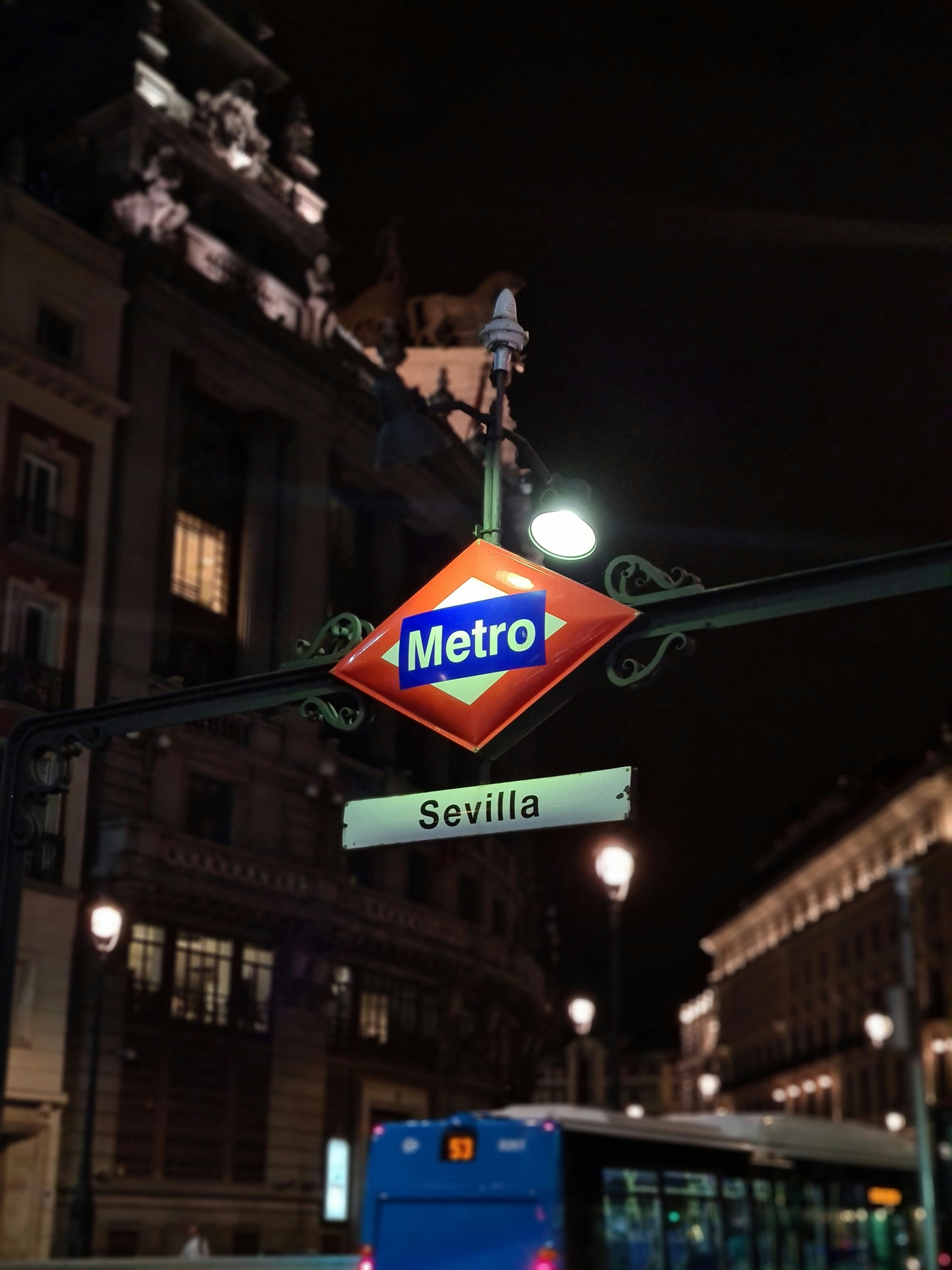Metro sign called "Sevilla" in Madrid, Spain at nighttime with a bus driving by