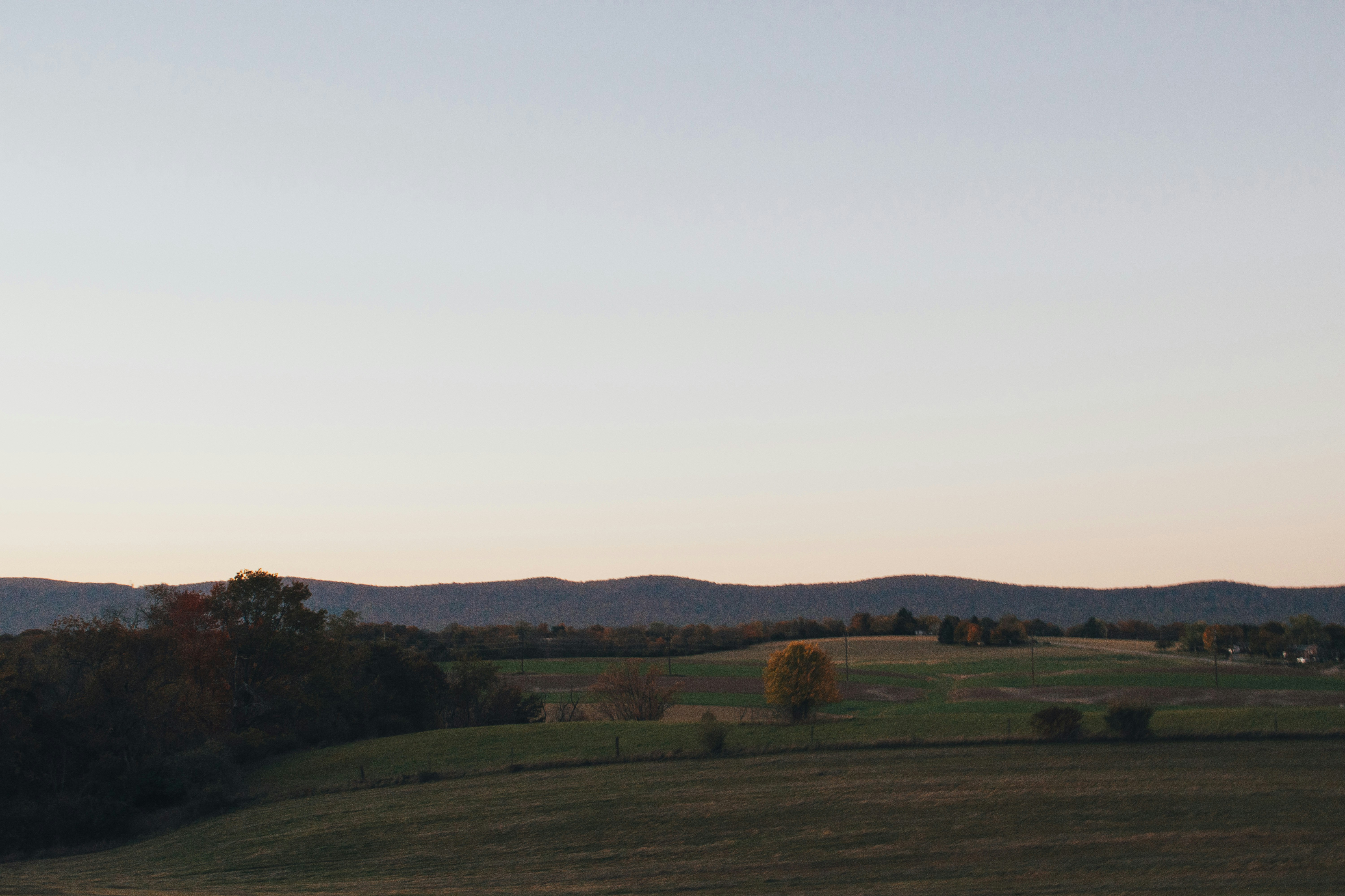 Serene landscape featuring gentle hills and a fading sky, capturing the tranquility of twilight. Trees dot the foreground, adding depth to the scene.