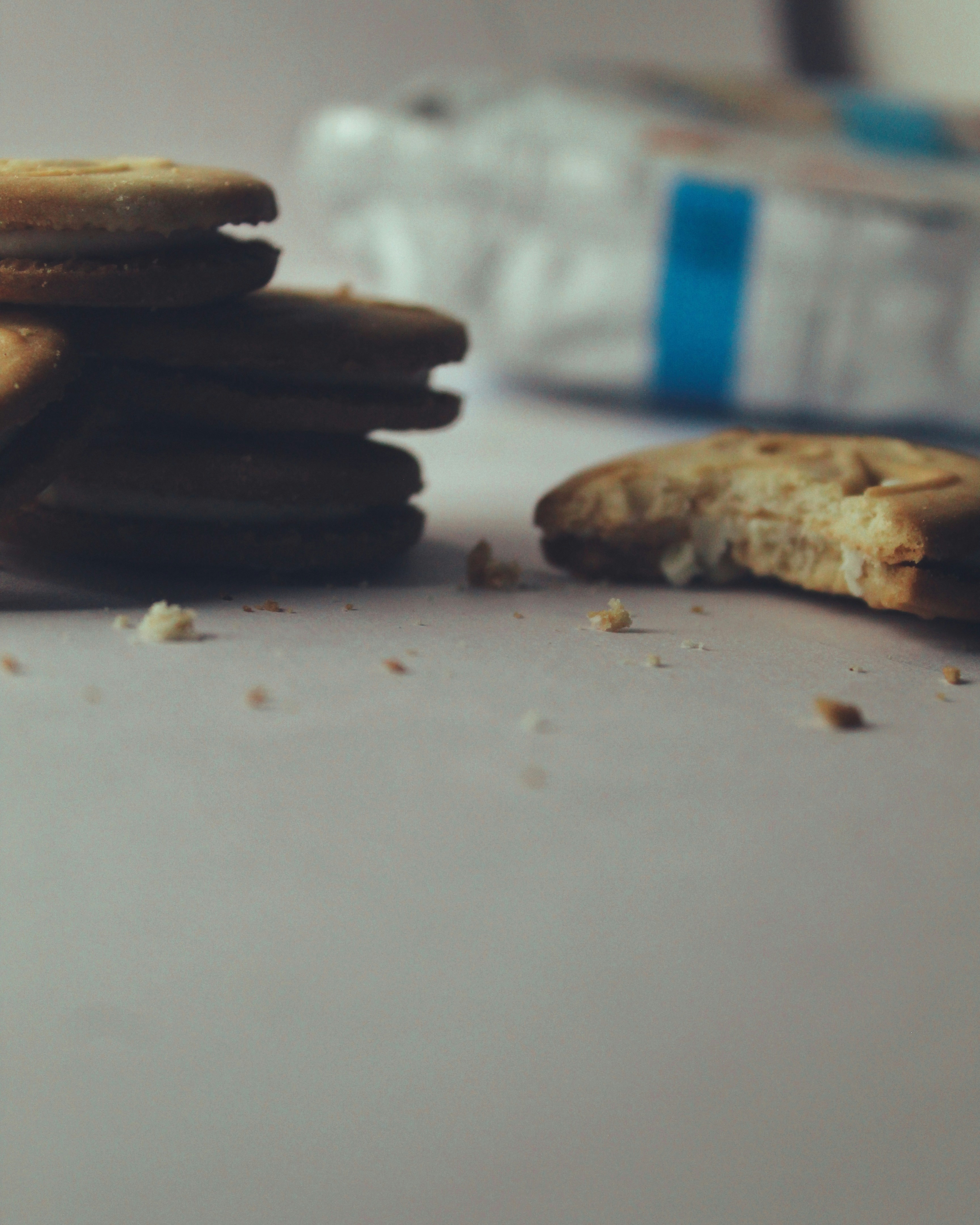 Stack of cookies with one partially eaten, scattered crumbs on a light surface. The background features a blurred snack package.