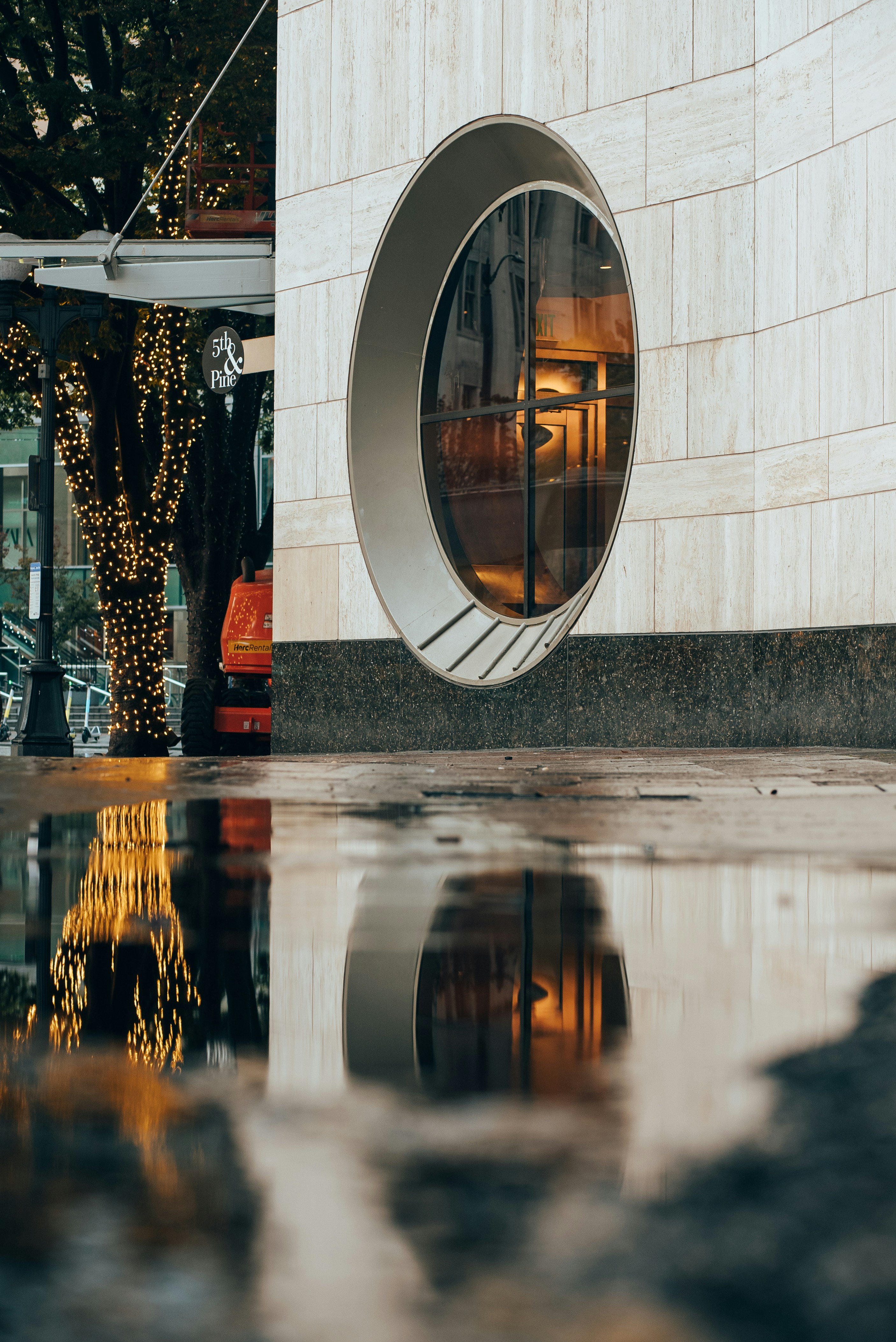 Circular Portal in Marble Facade Mirrors a Rain-Washed City Street