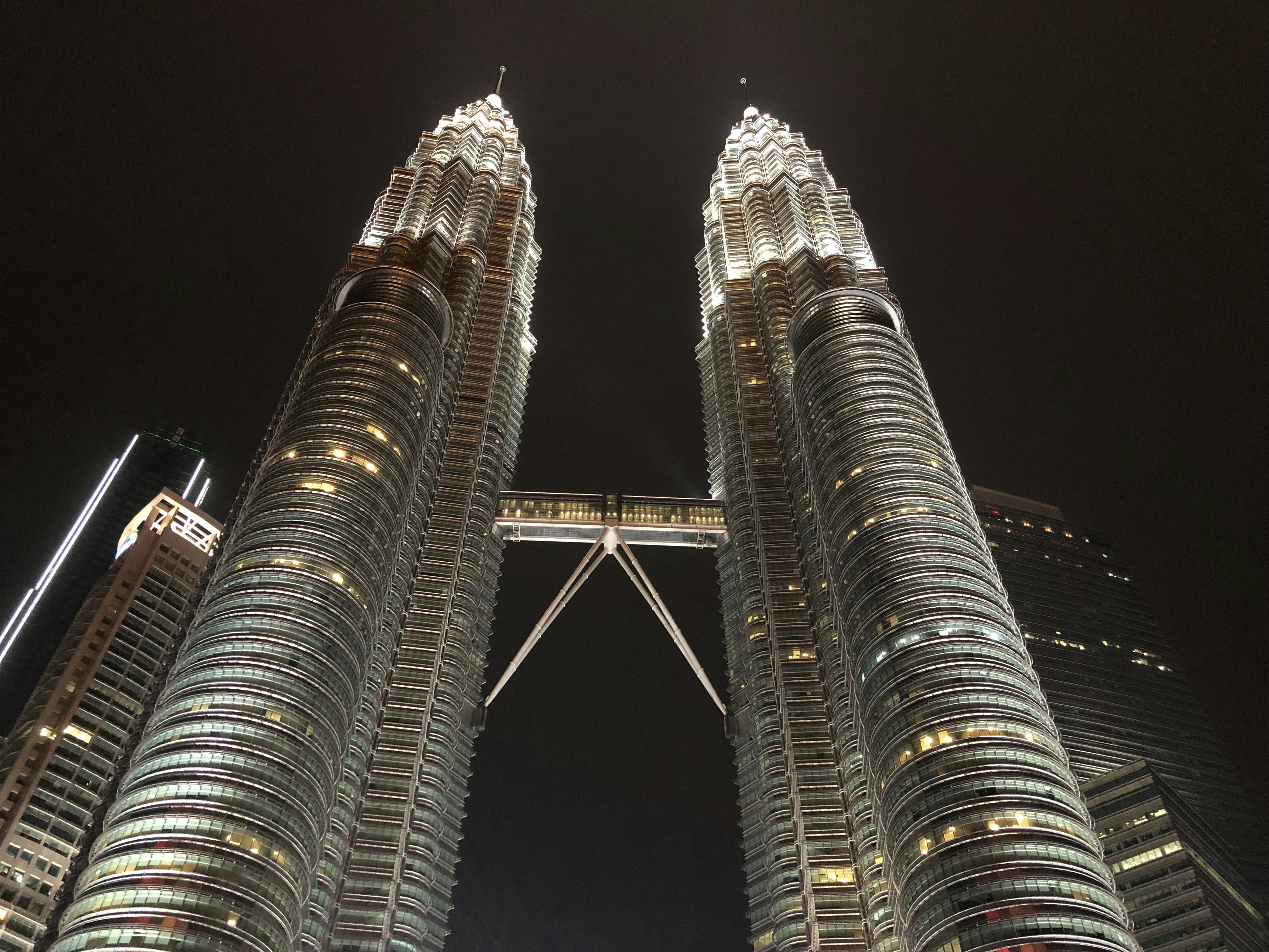 My flight got in pretty late and knowing my schedule the next day I knew the only chance I would have to see these towers was if I went there late at night. It was only a mile walk from my hotel so to the street I went on foot. Despite a downpour I loved seeking down town Kuala Lumpur and seeking the Petronas Towers in all their magnificent hight! | a couple of tall buildings with Petronas Towers in the background
