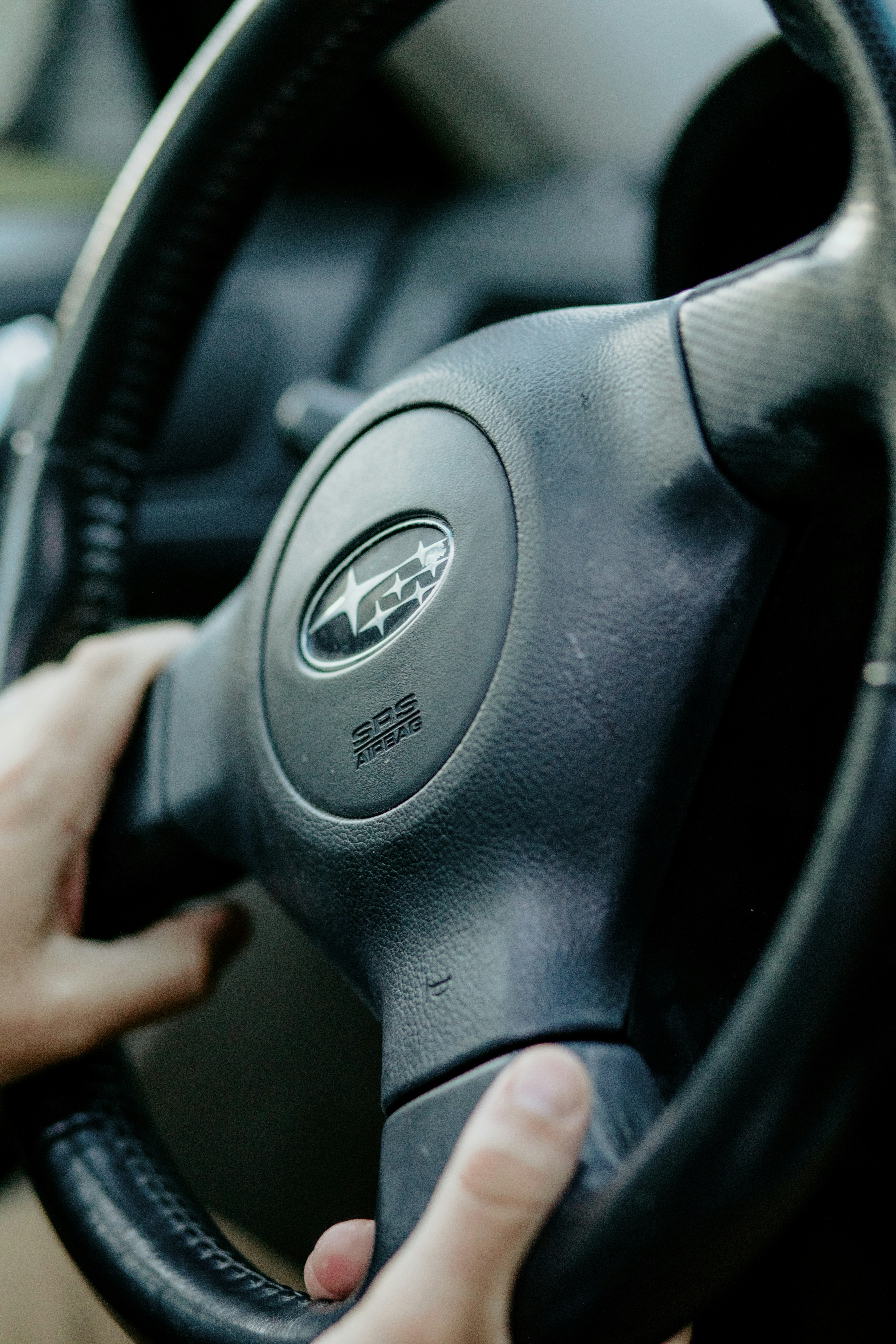 Subaru Emblem in the Grip: Close-Up of a Driver's Hands on the Wheel