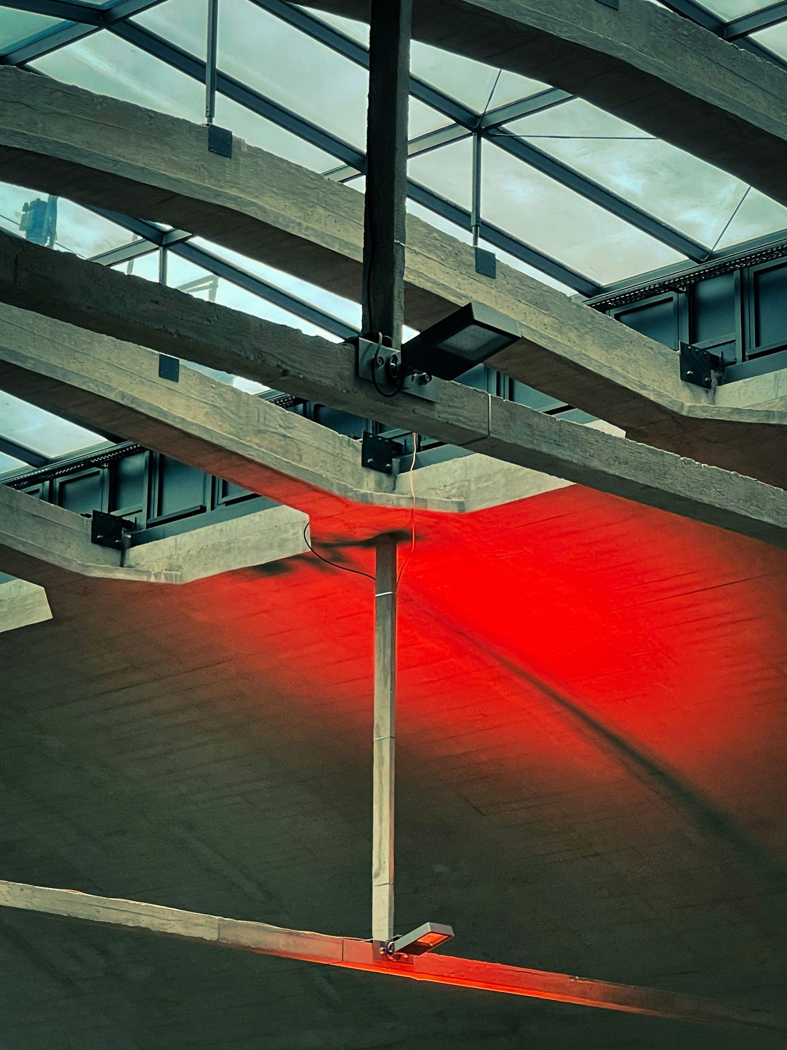 Red light traced along concrete beams in a sunlit industrial atrium