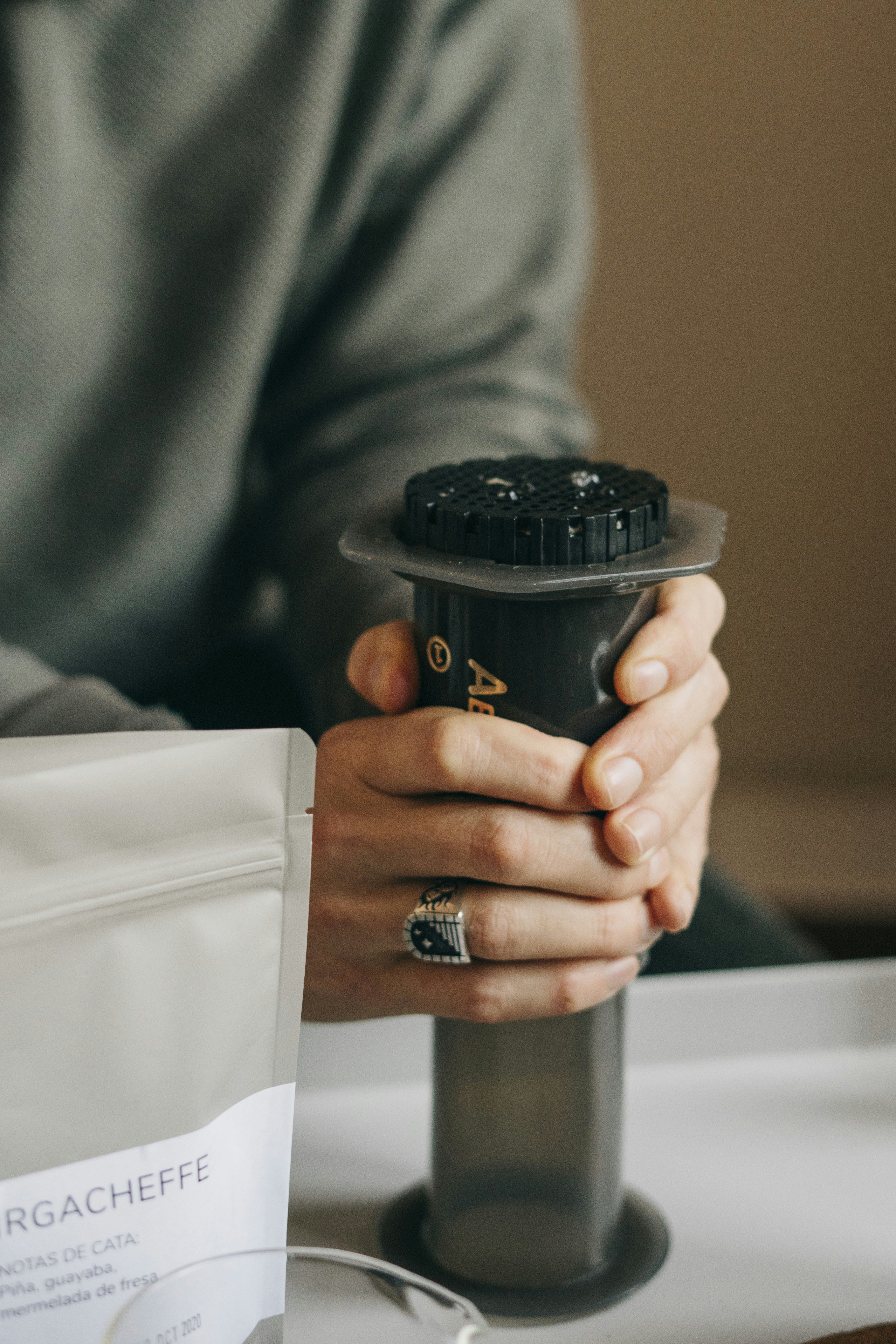 Hands gripping an Aeropress, preparing to brew coffee, with a bag of Ethiopian coffee beans nearby.