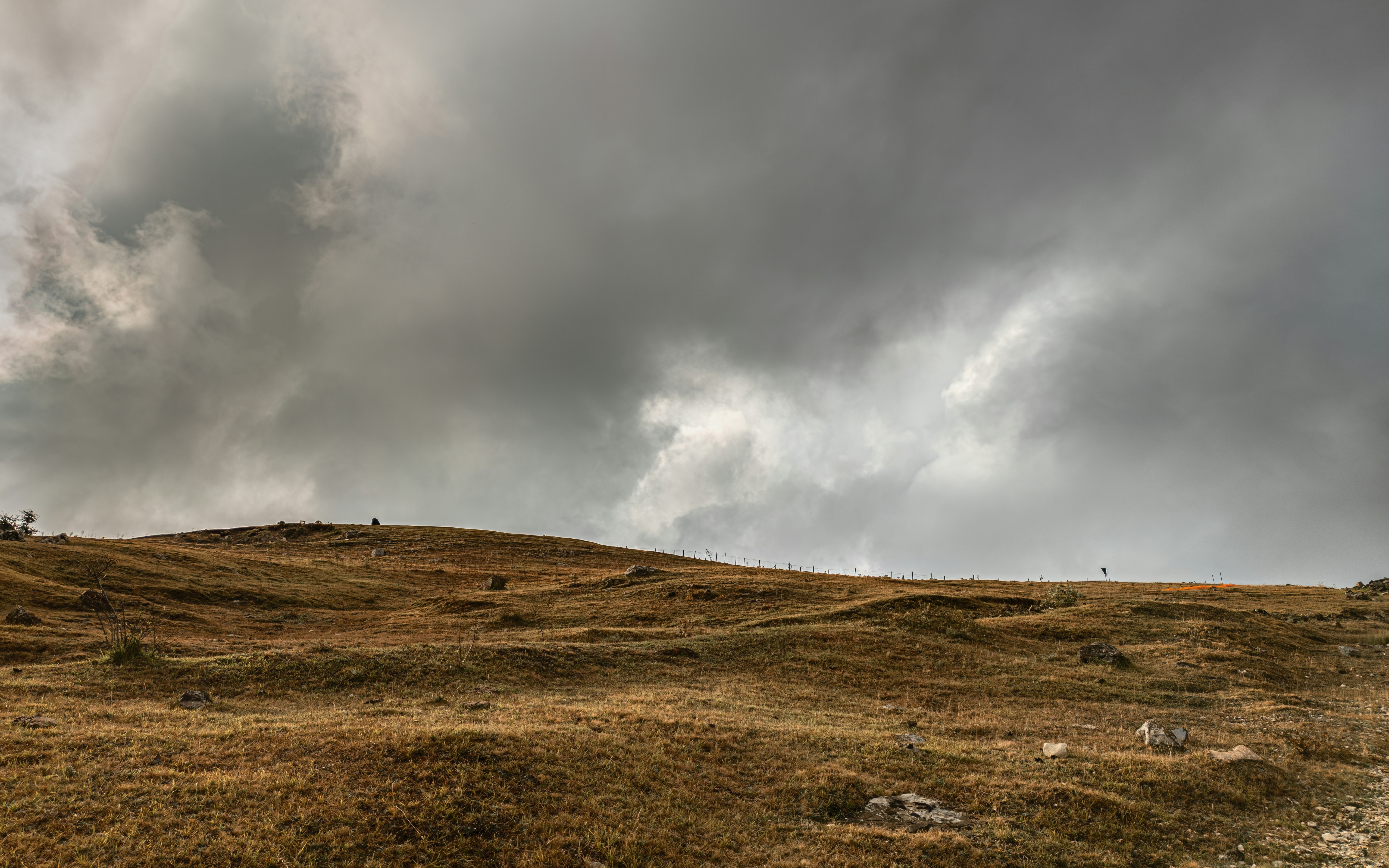 Expansive hillside under a dramatic, cloud-filled sky, showcasing the interplay between light and shadow across the terrain.