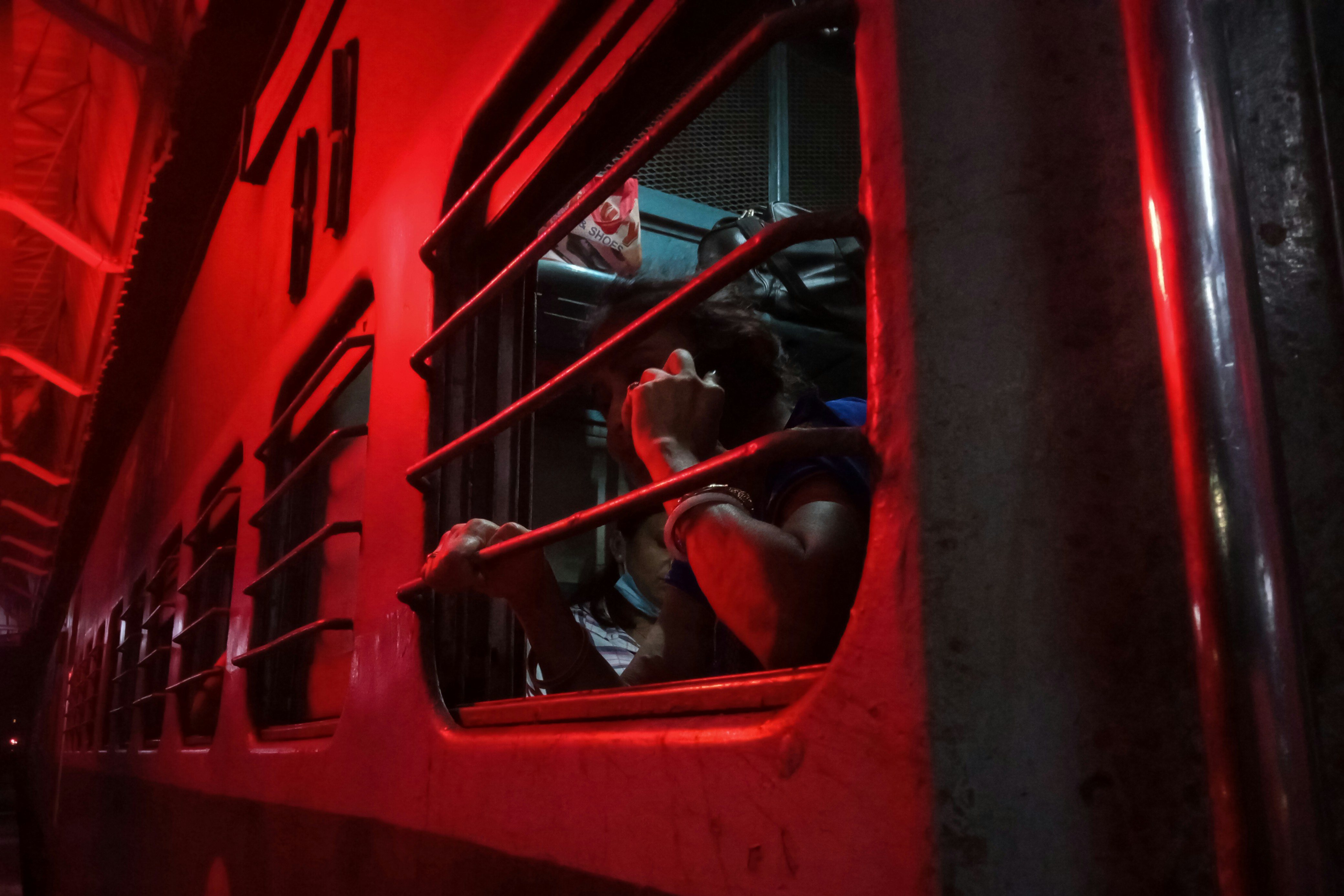 A passenger gazes out from a train window, illuminated by red interior lights, capturing a moment of contemplation during a nighttime journey.