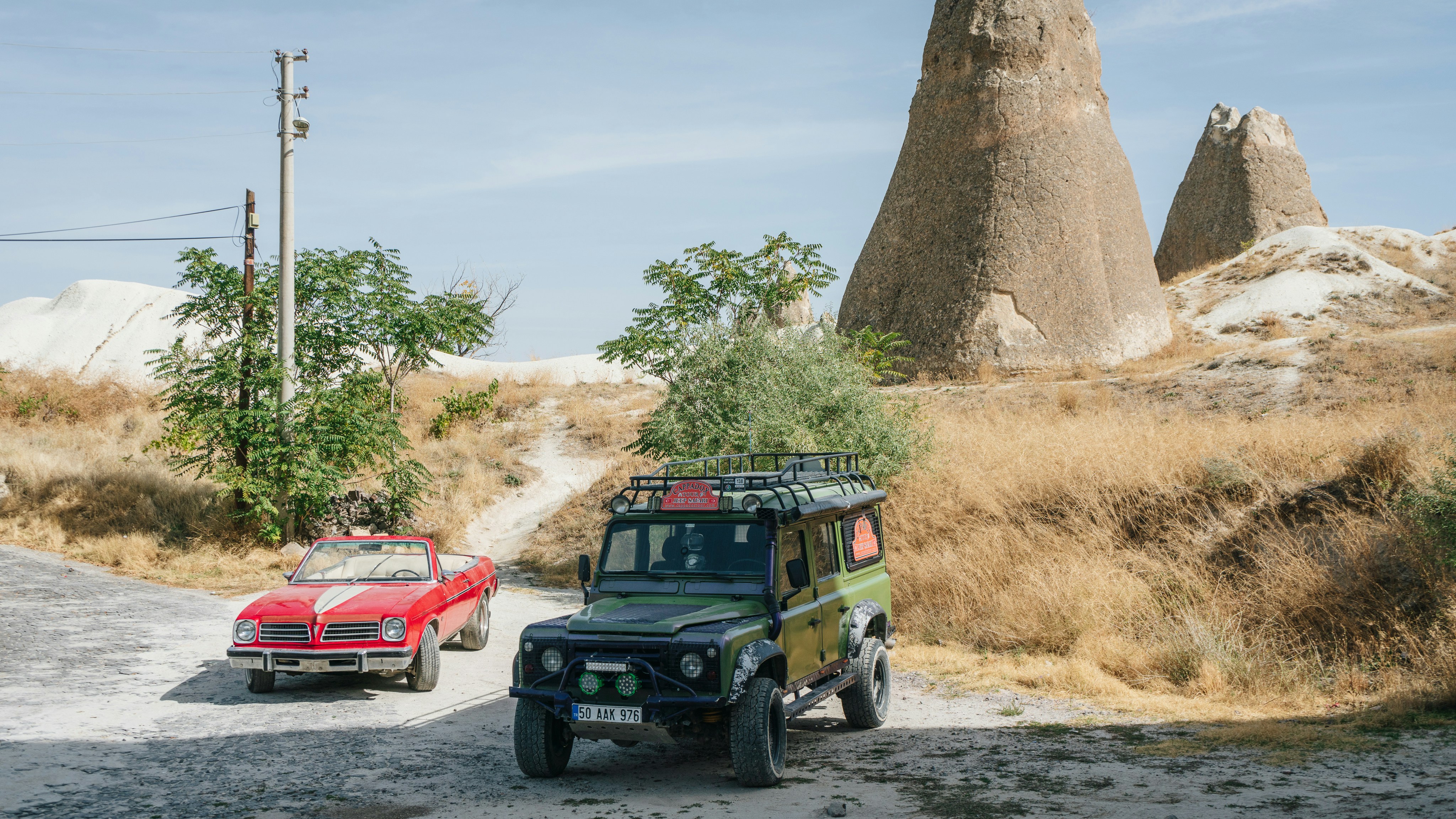 Hoodoo Horizon: Green Defender and Red Classic on a Dusty Desert Road