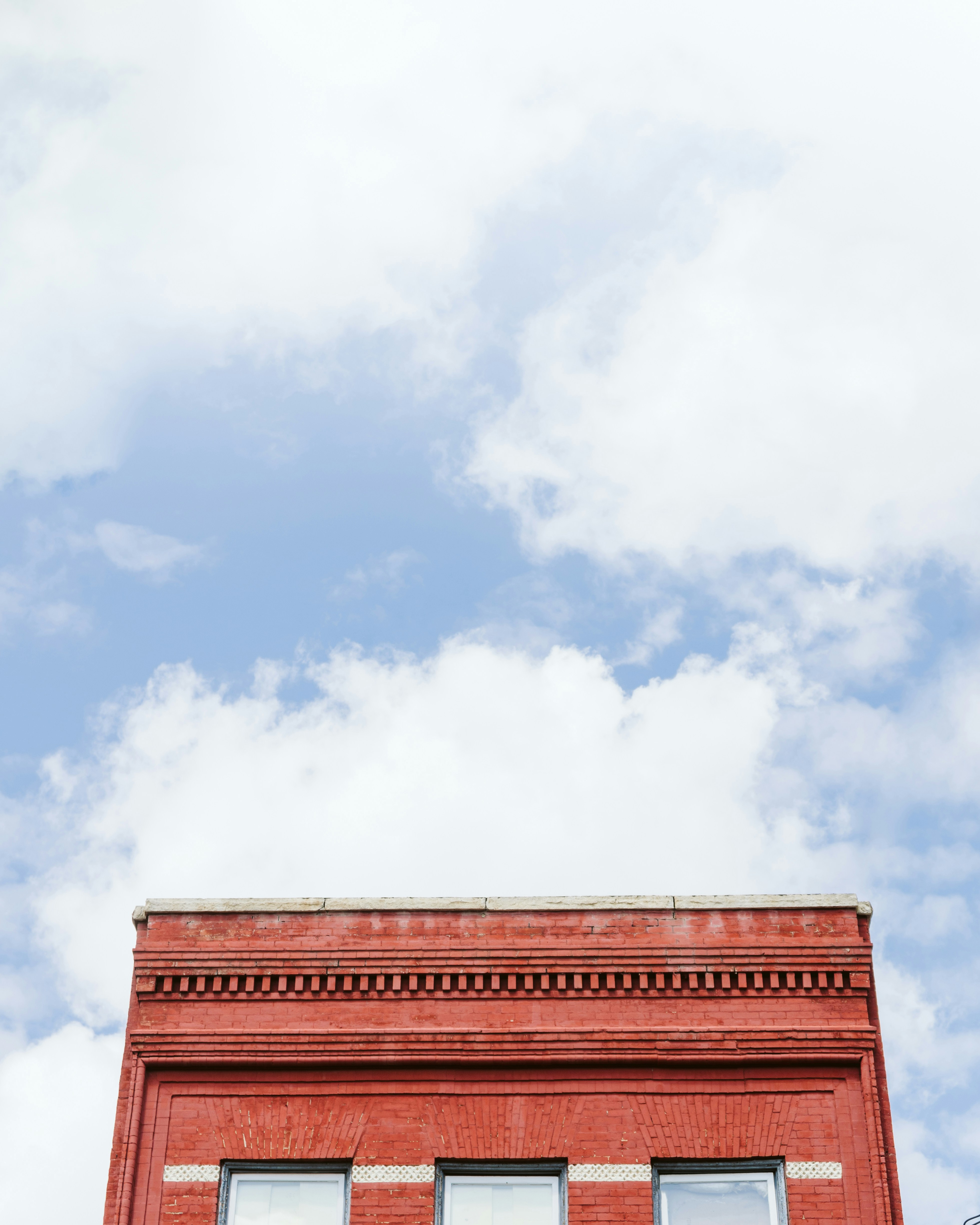 Vibrant red brick building with large windows under a bright blue sky dotted with fluffy clouds.