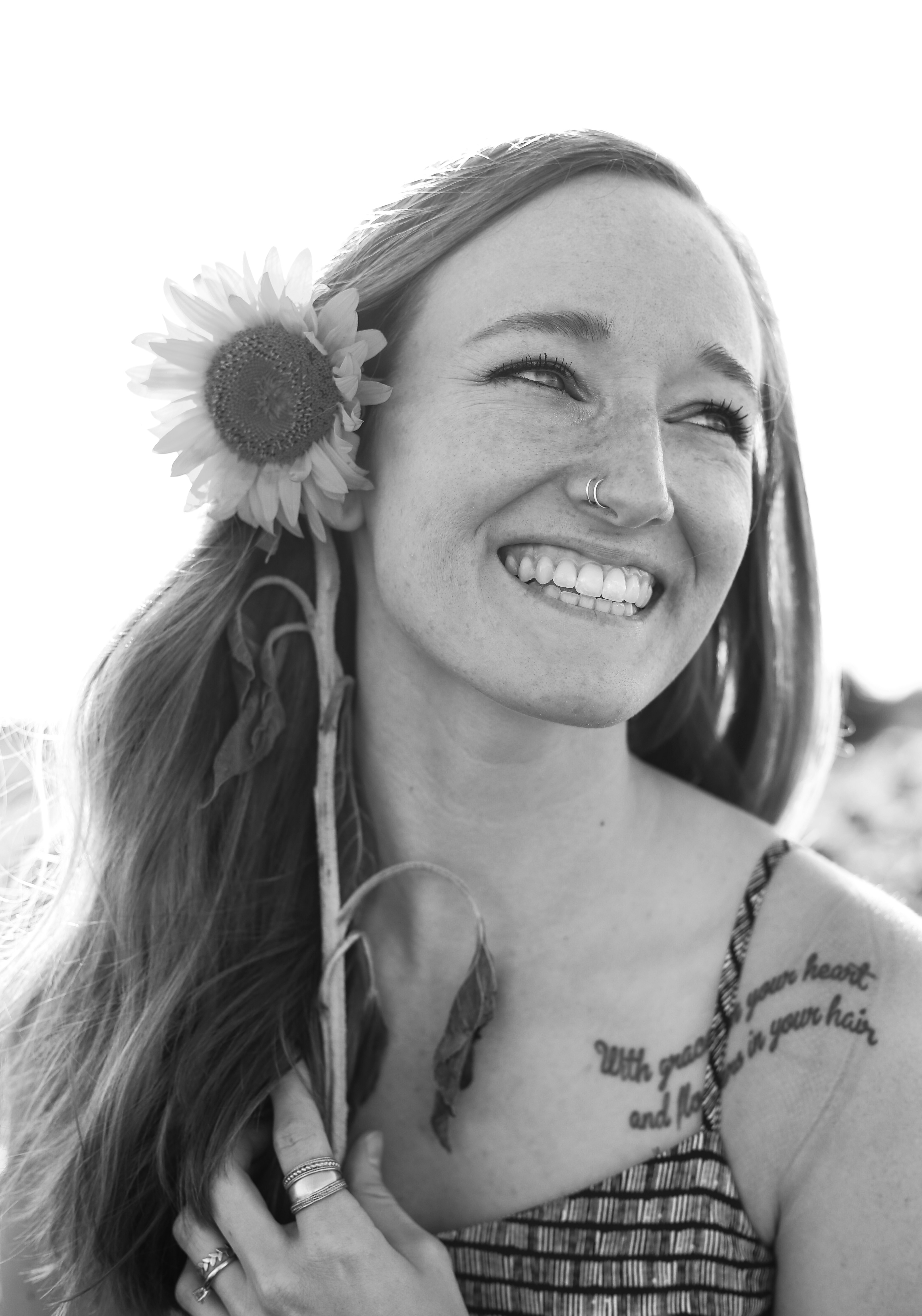 Sunflower Halo: A sunlit beach portrait of a smiling, tattooed woman.