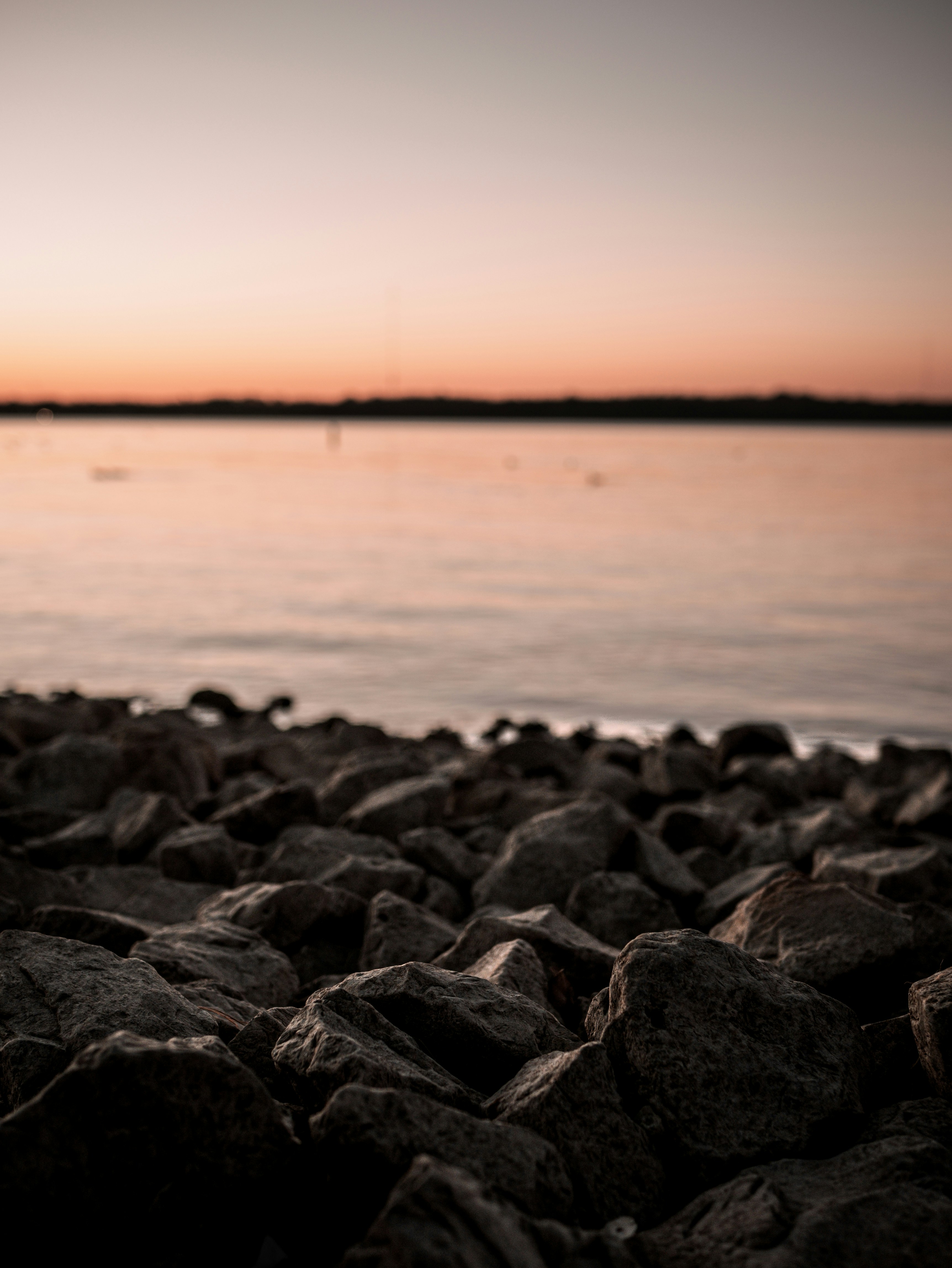 Rocky shoreline at dusk with a tranquil water backdrop and a fading sunset sky.