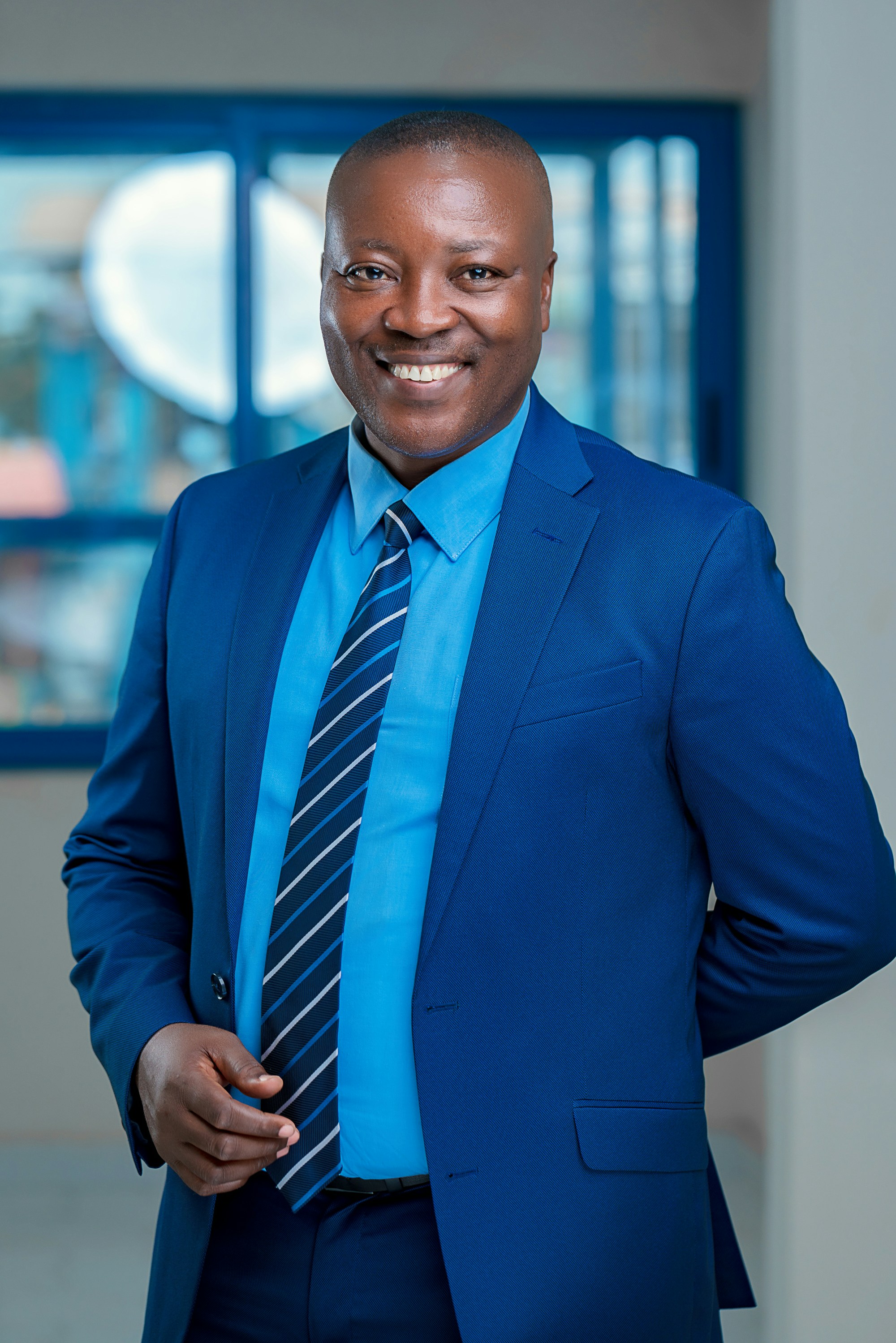 A well-dressed man in a blue suit, exuding confidence with a warm smile in a modern office setting.