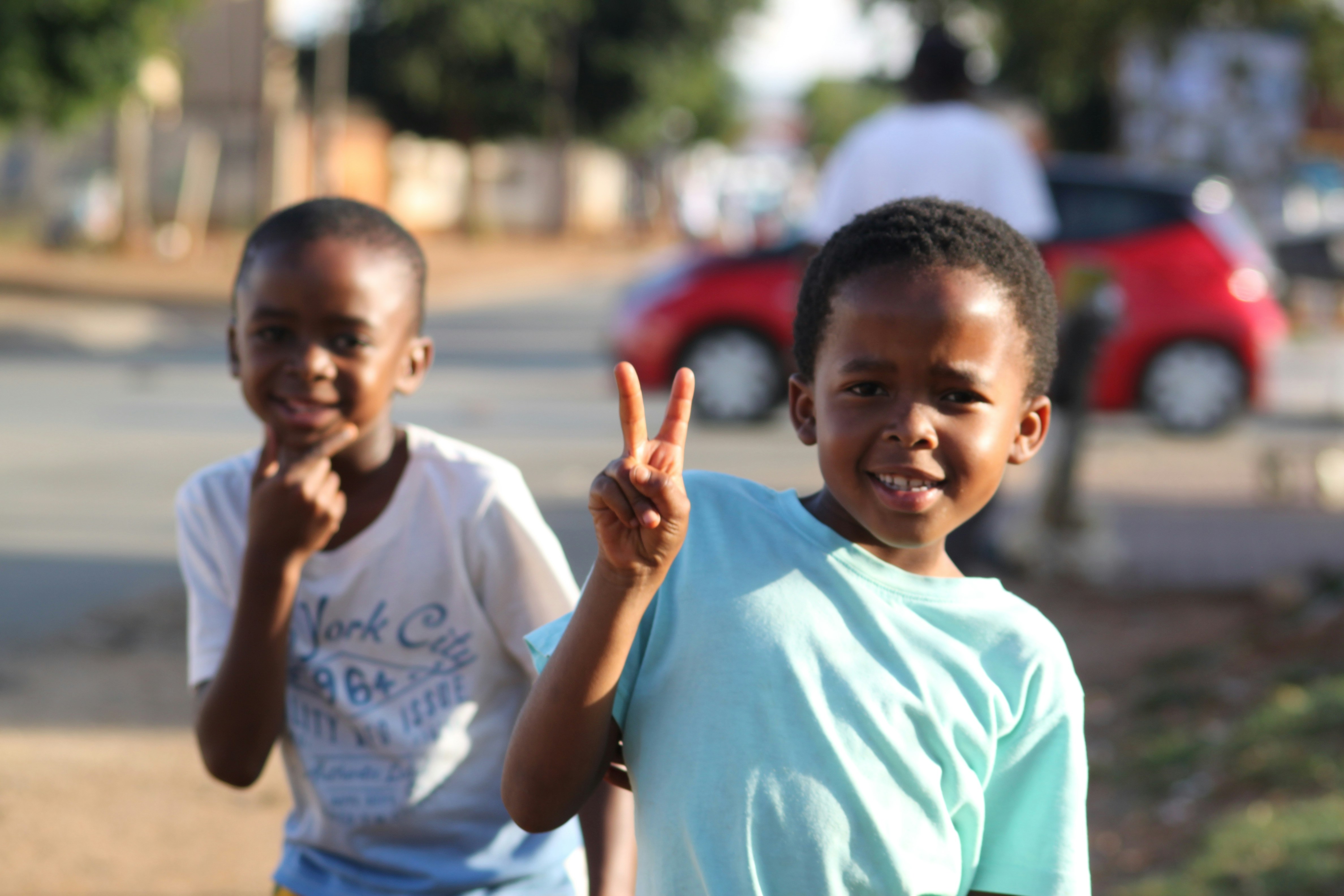 Two boys cheerfully pose, one flashing a peace sign, with a blurred urban backdrop.