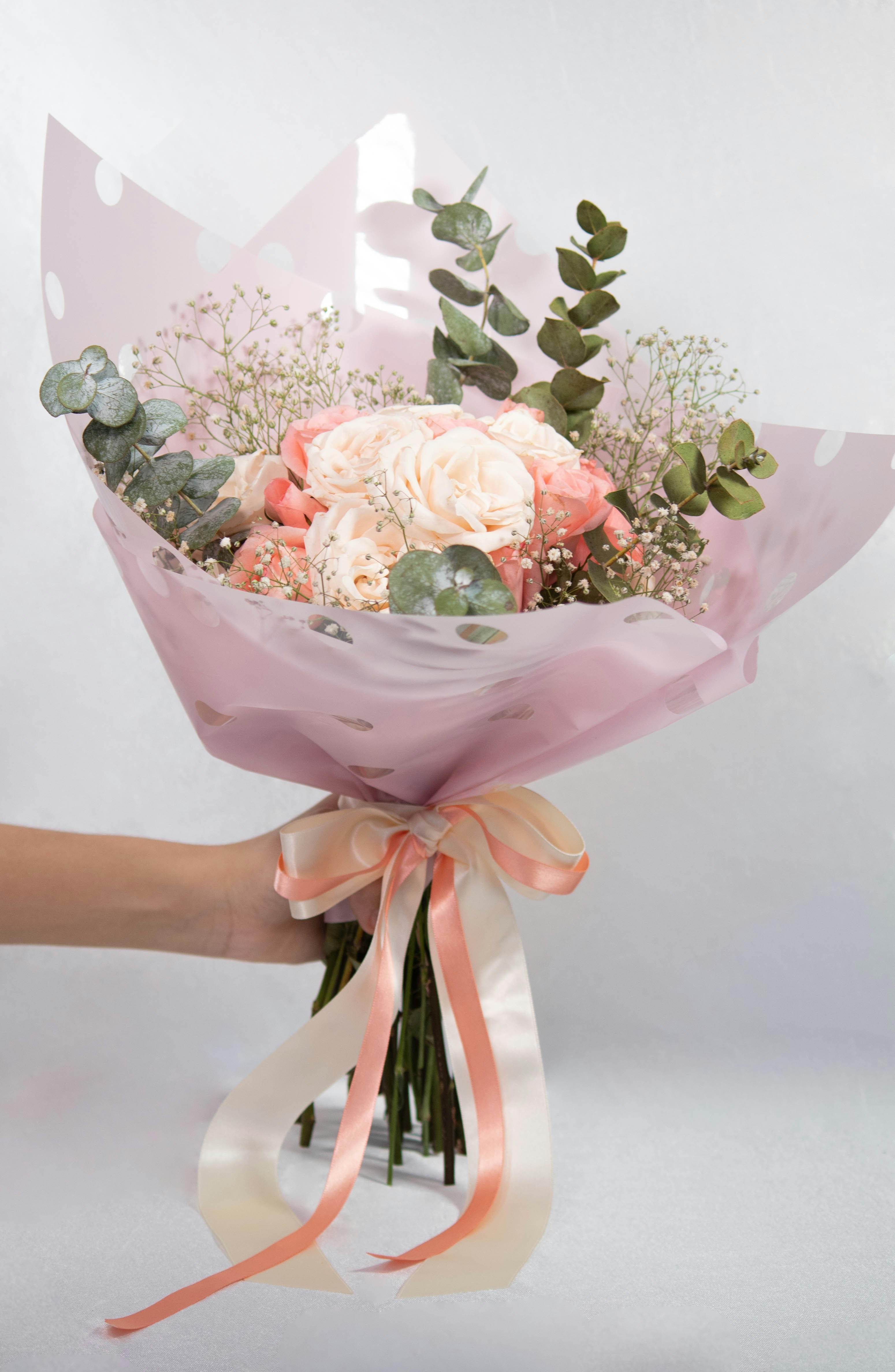 Blush bouquet in soft pink wrap, held aloft by a pastel ribbon