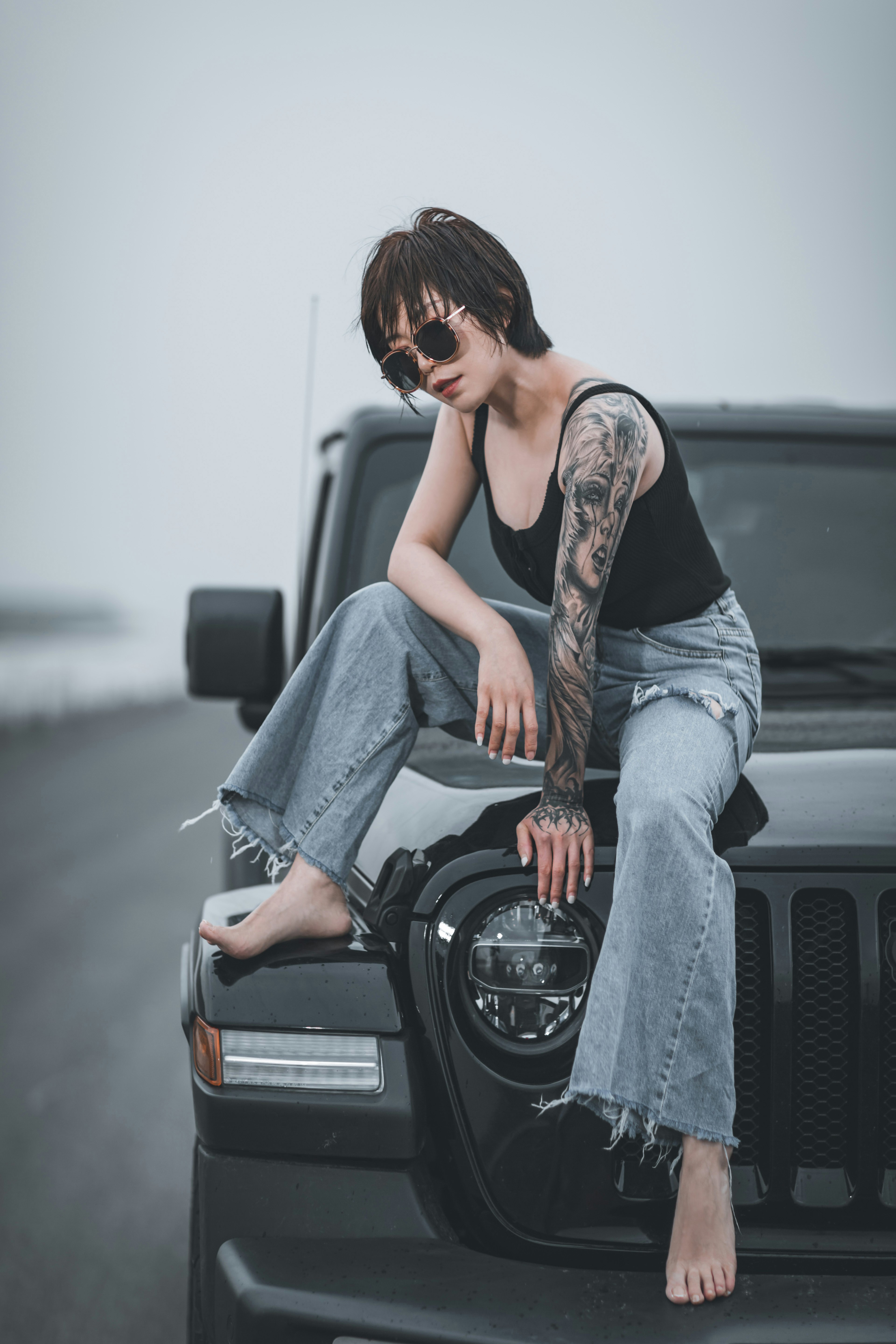Barefoot on the Hood: Tattooed Confidence on a Moody Coastal Road