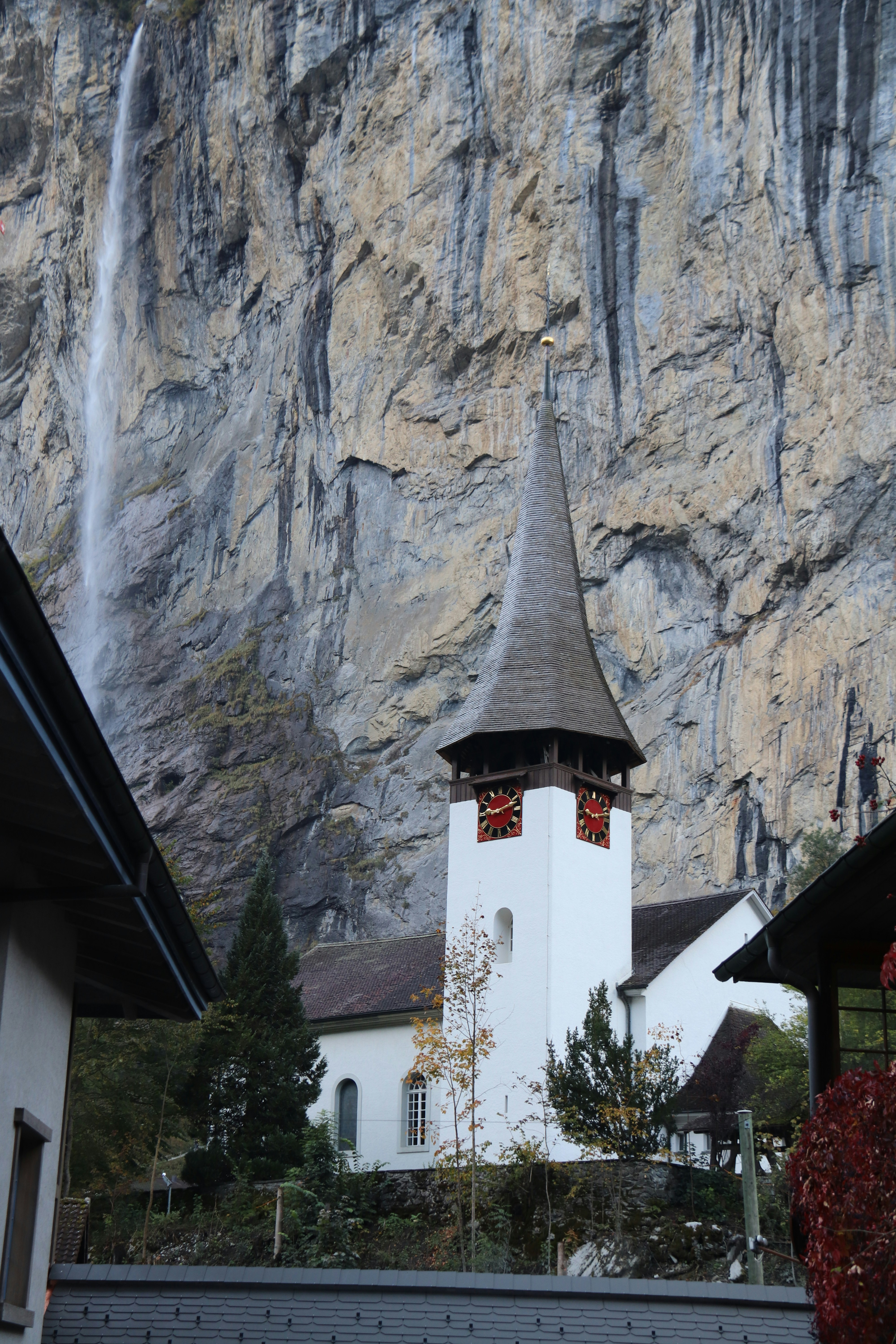 Stone Cliff Sanctuary: A White-Steepled Church Nestled at the Foot of a Towering Cliff