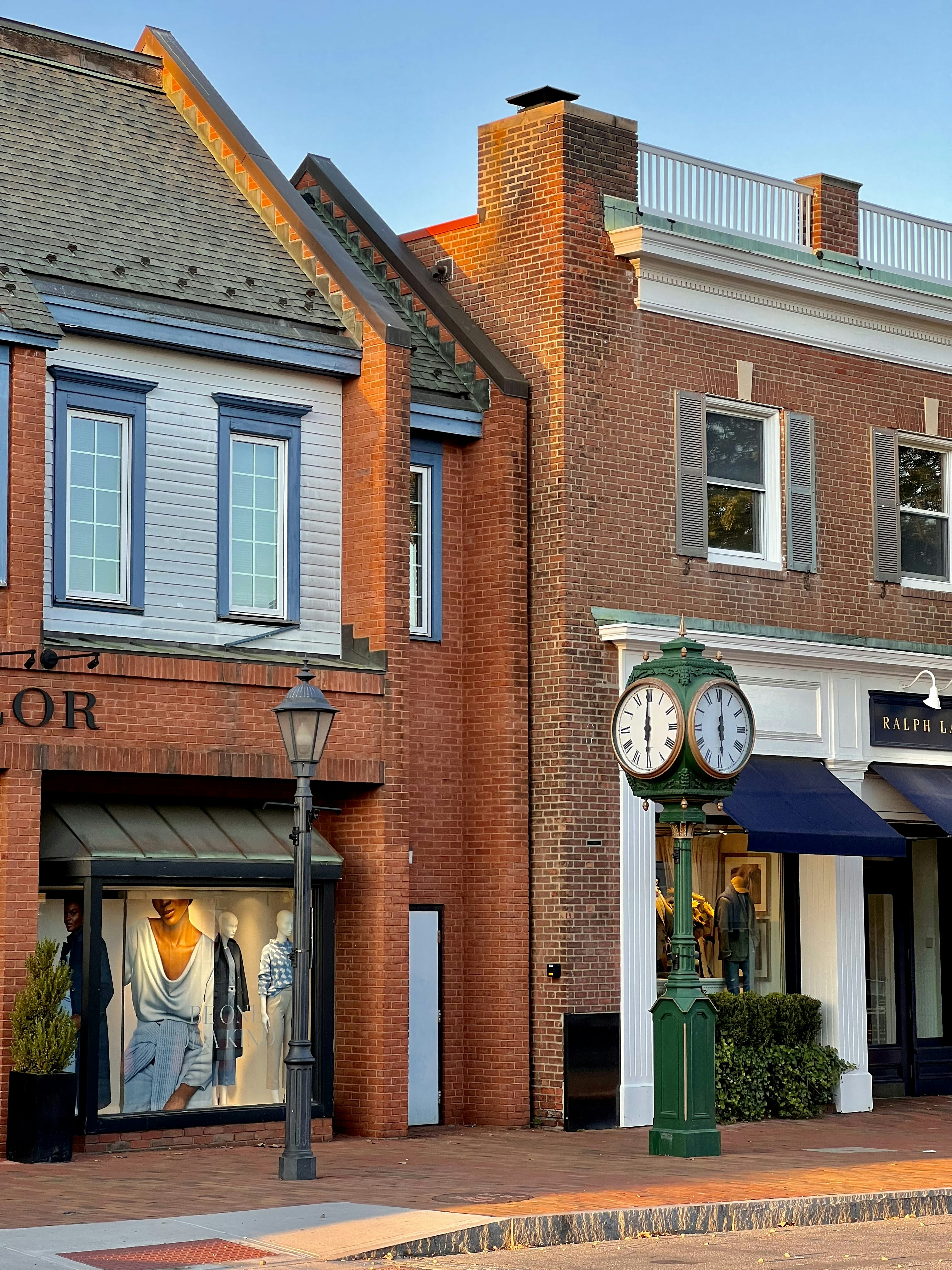 Storefronts with classic architecture bathed in warm sunset light, featuring a vintage street clock.