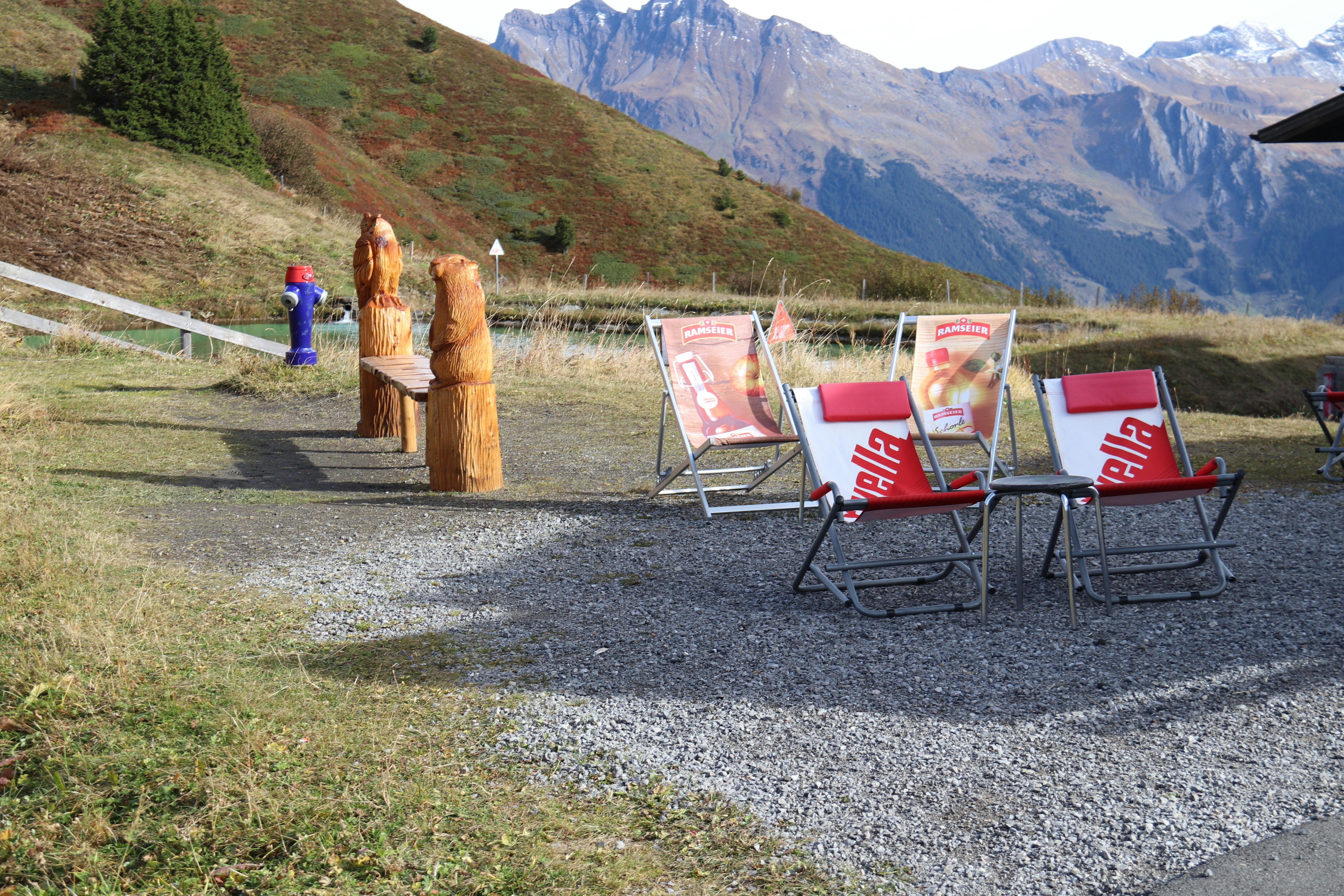Sunlit Adirondack Mirage: Deck Chairs and Stone Figures Against Alpine Backdrop