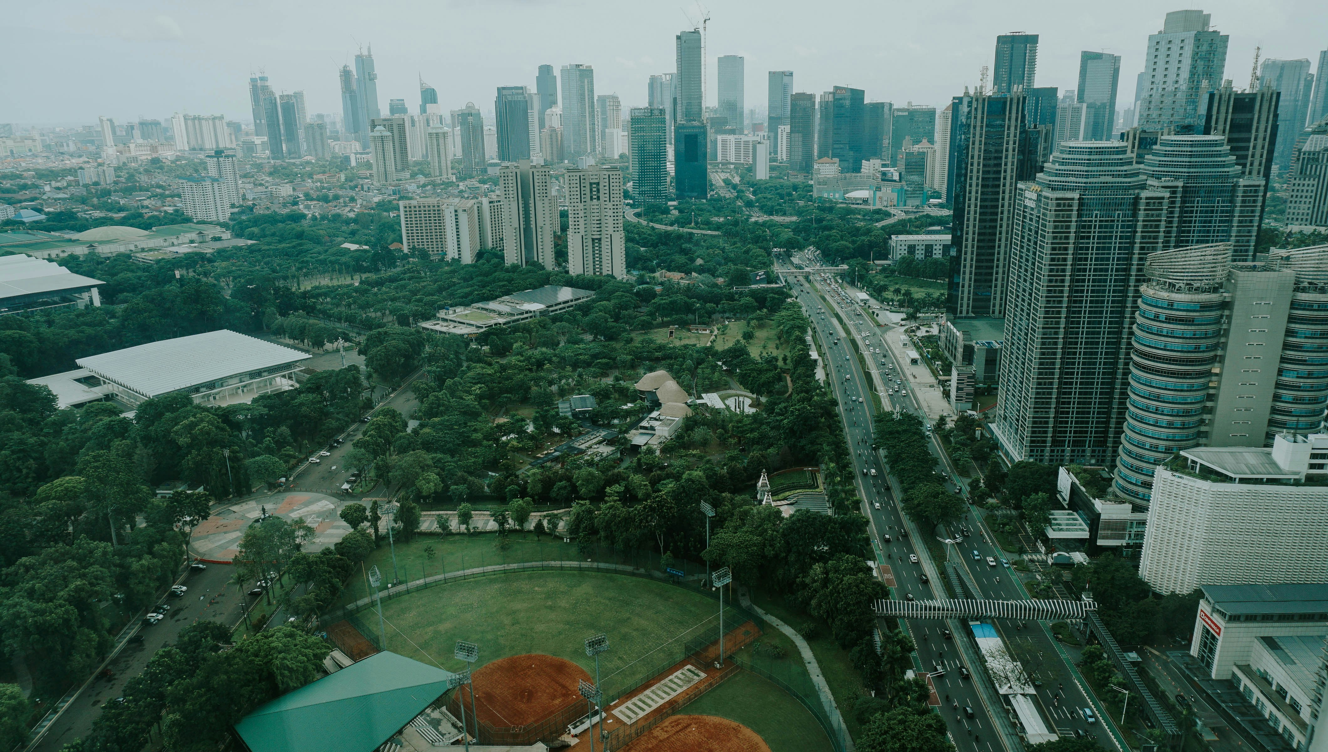 Expansive view of Jakarta's skyline with a mix of high-rise buildings and green spaces under an overcast sky.