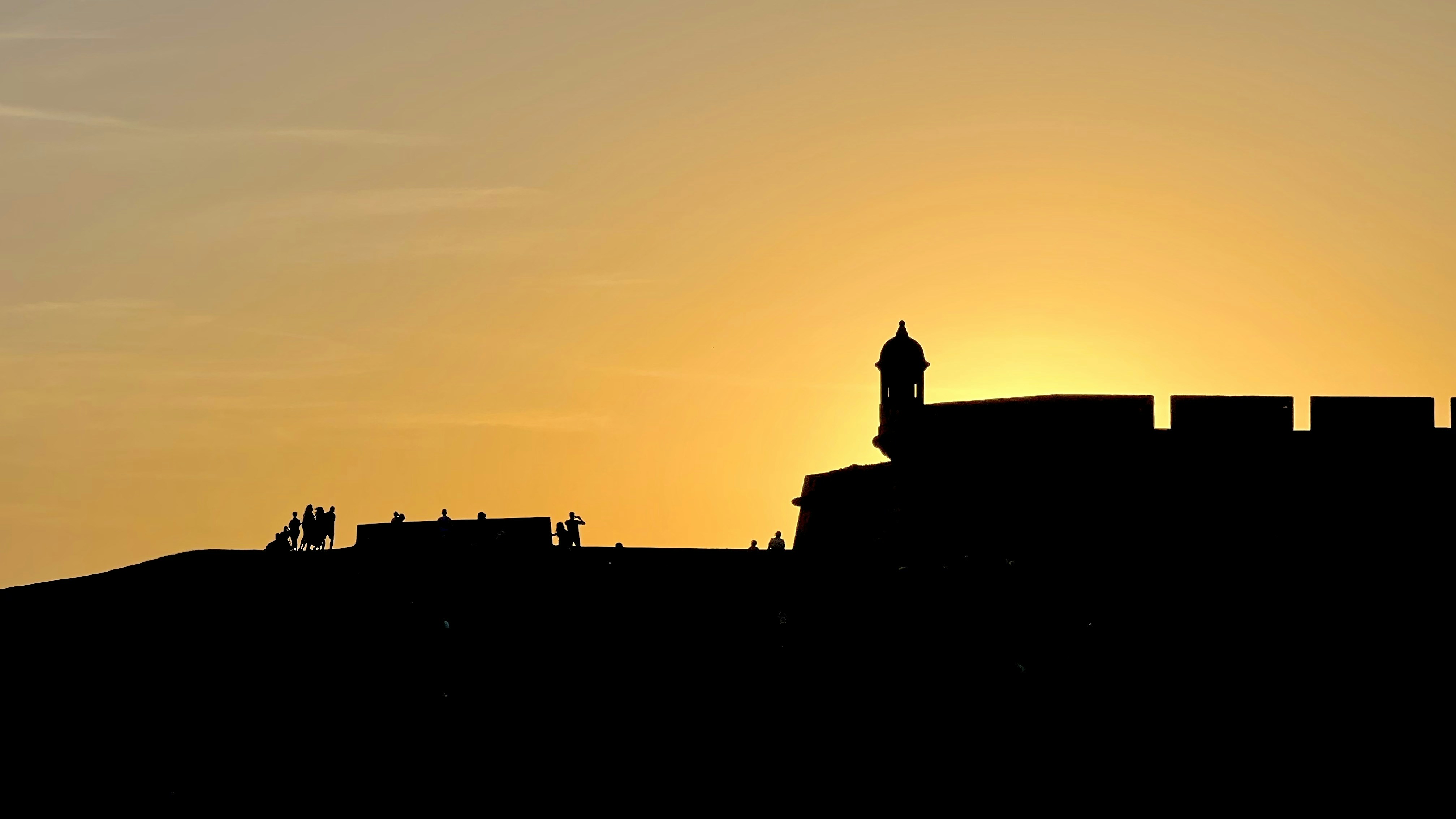 Silhouetted fort and figures against a vibrant orange sunset sky.