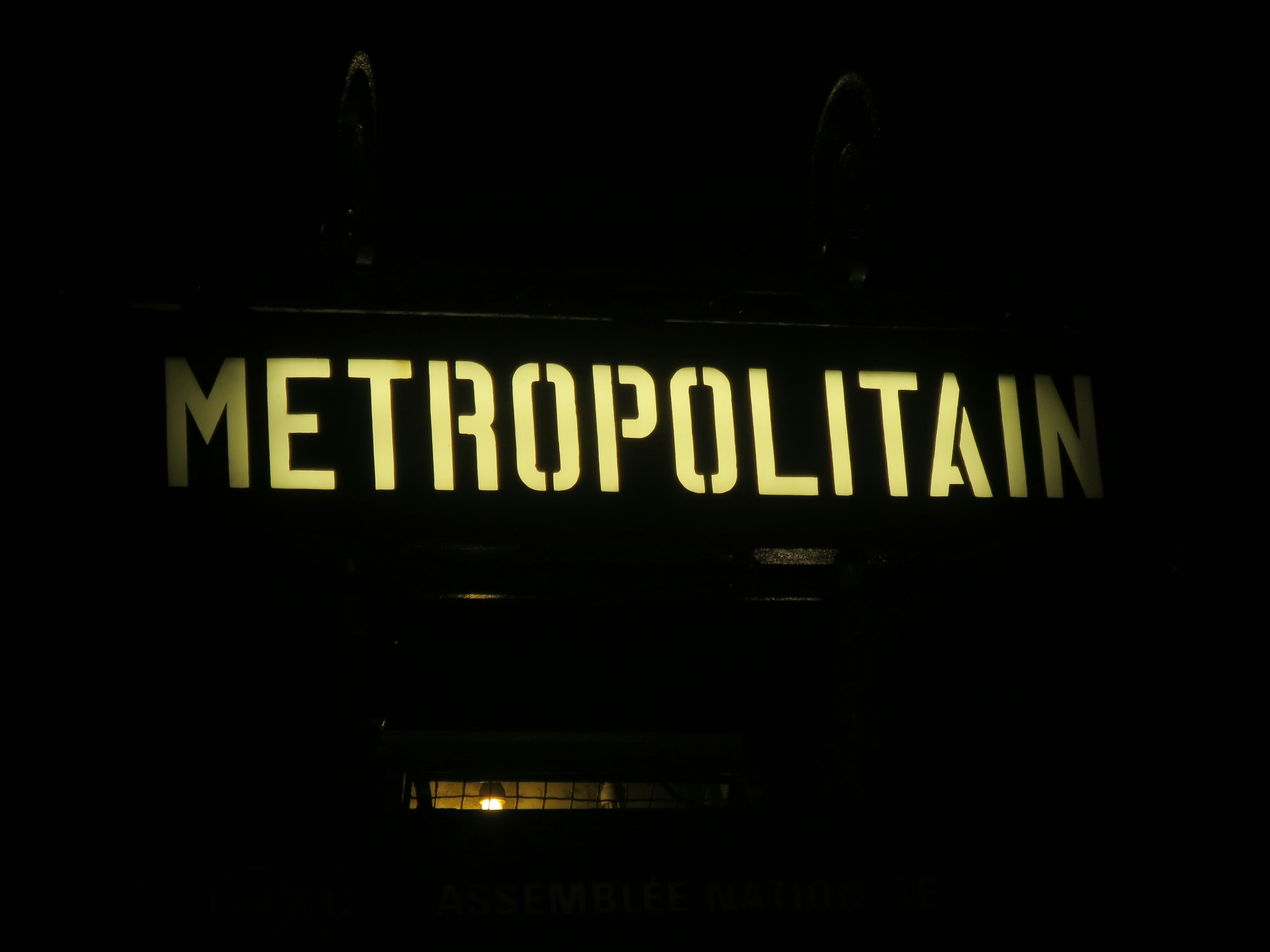 Night photograph of a glowing Metropolitain sign, with a warm yellow glow spilling from a small window beneath.