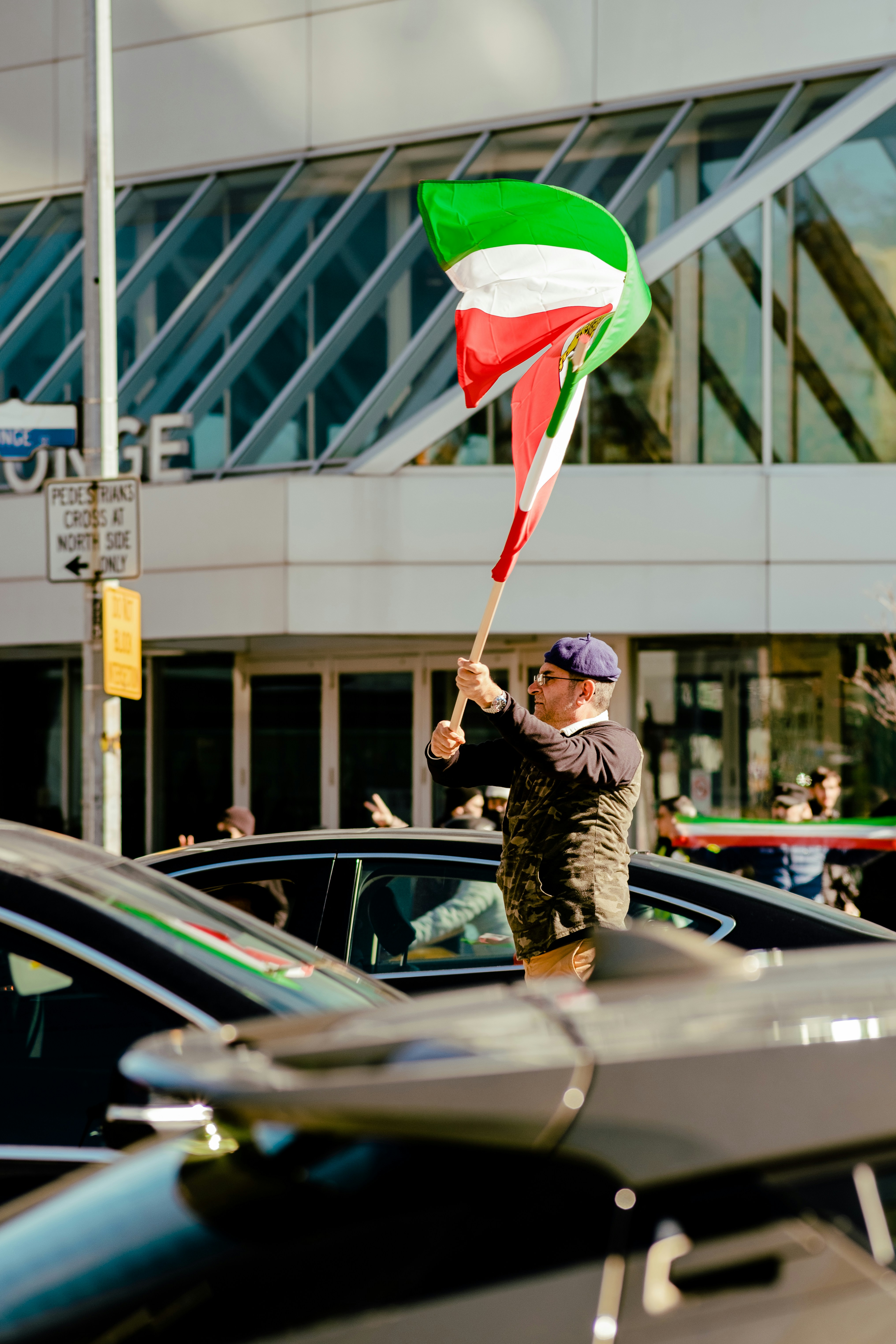 Man enthusiastically waving an Italian flag amidst a festive crowd and cars. The urban backdrop adds to the celebratory atmosphere.