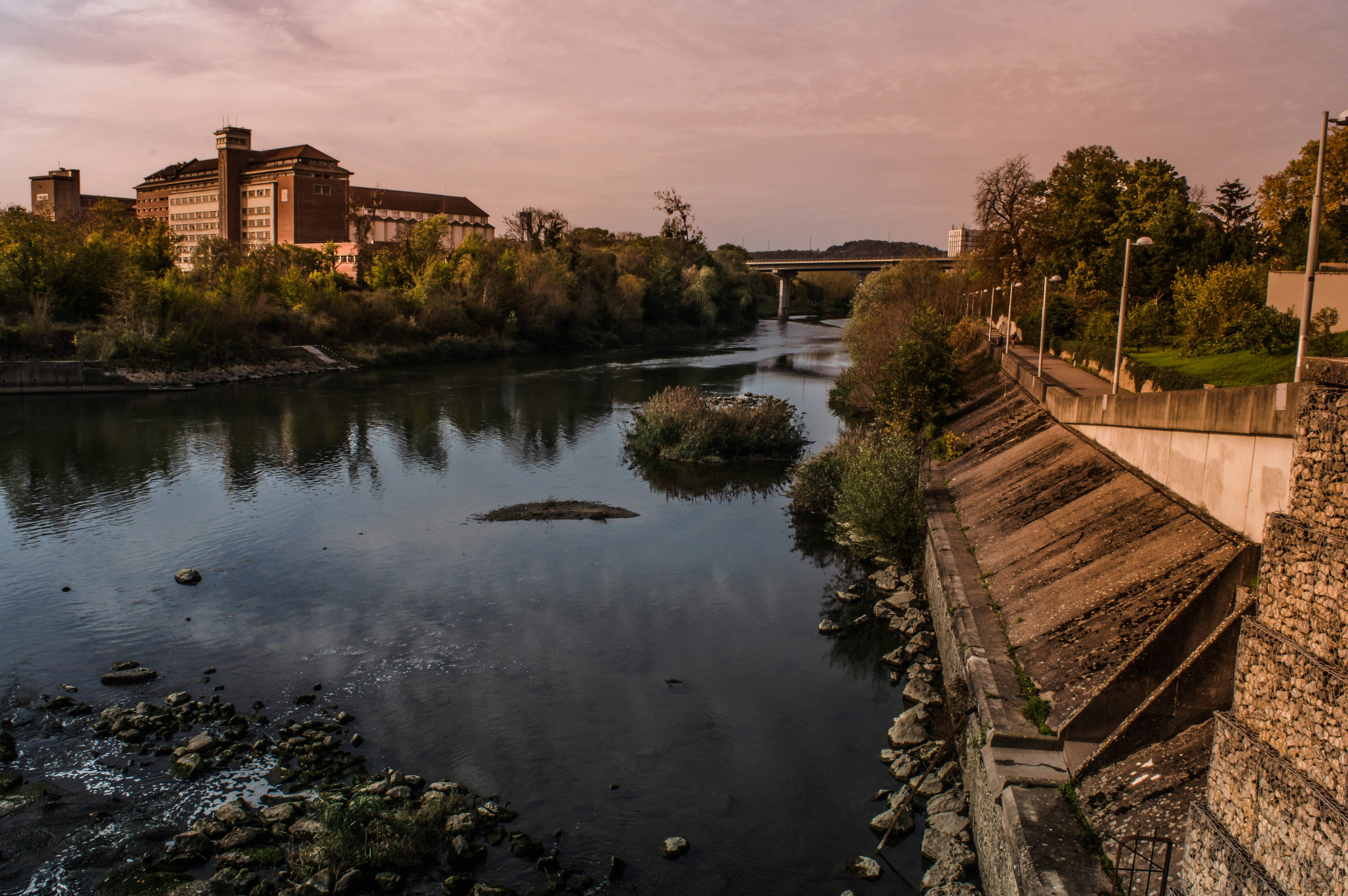 Dusk Along the Sloped Riverside Dam: Quiet Water Framed by Brick Mills