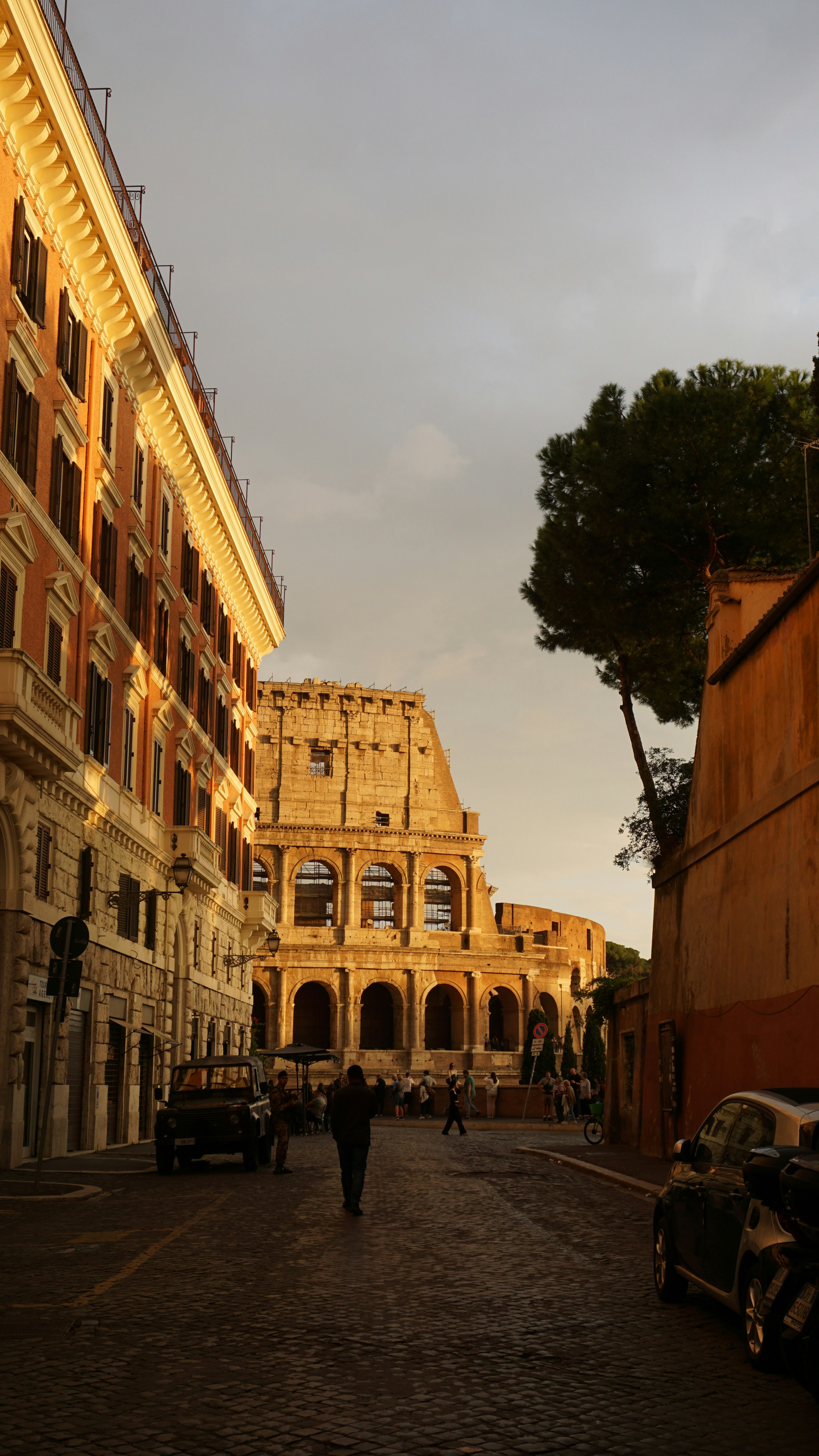 The Colosseum emerges majestically at dusk, framed by historic buildings and a cobblestone street, capturing the essence of Rome's rich heritage.