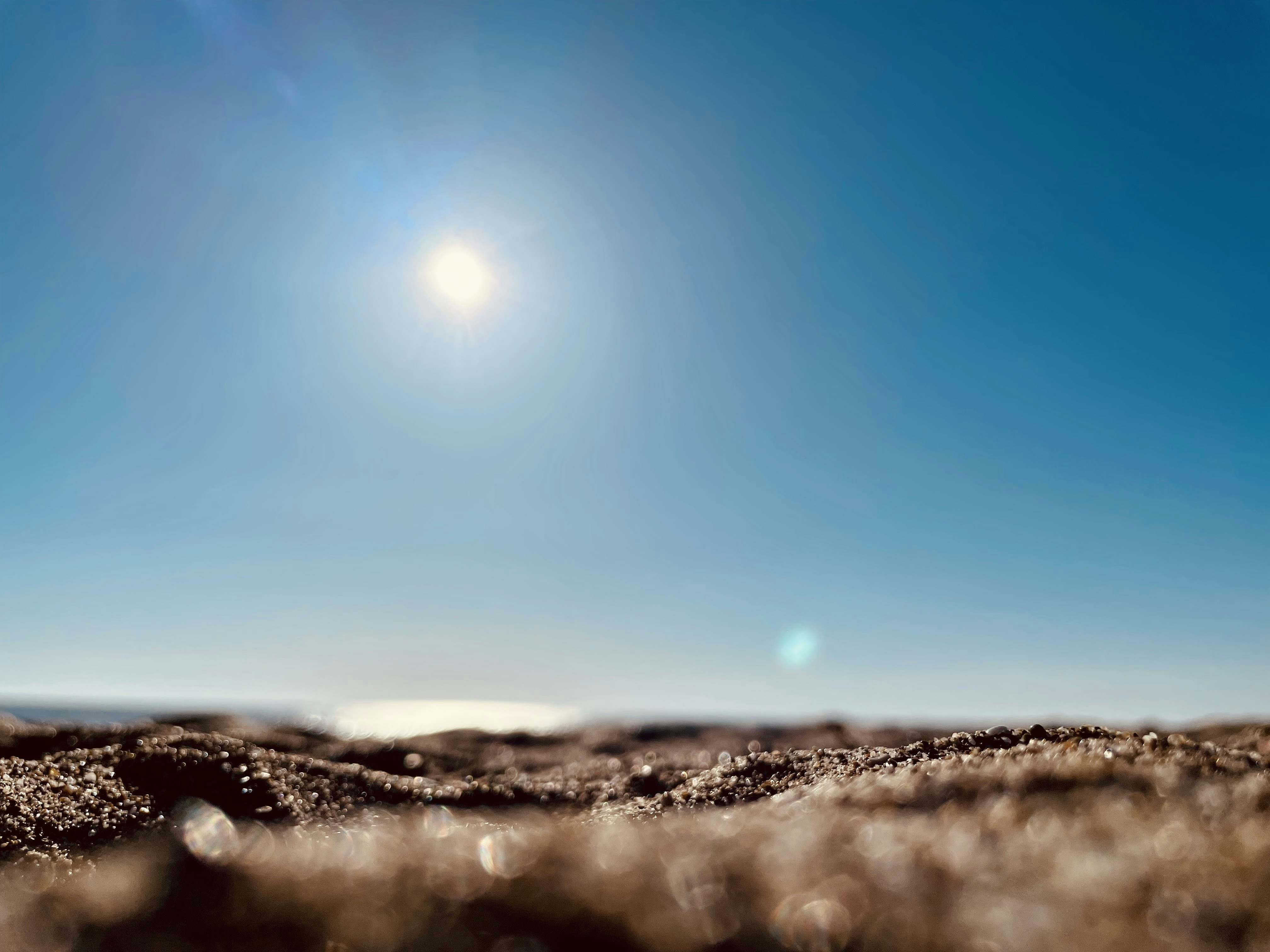 Low-angle view of a sunlit beach with a bright sun against a clear blue sky.