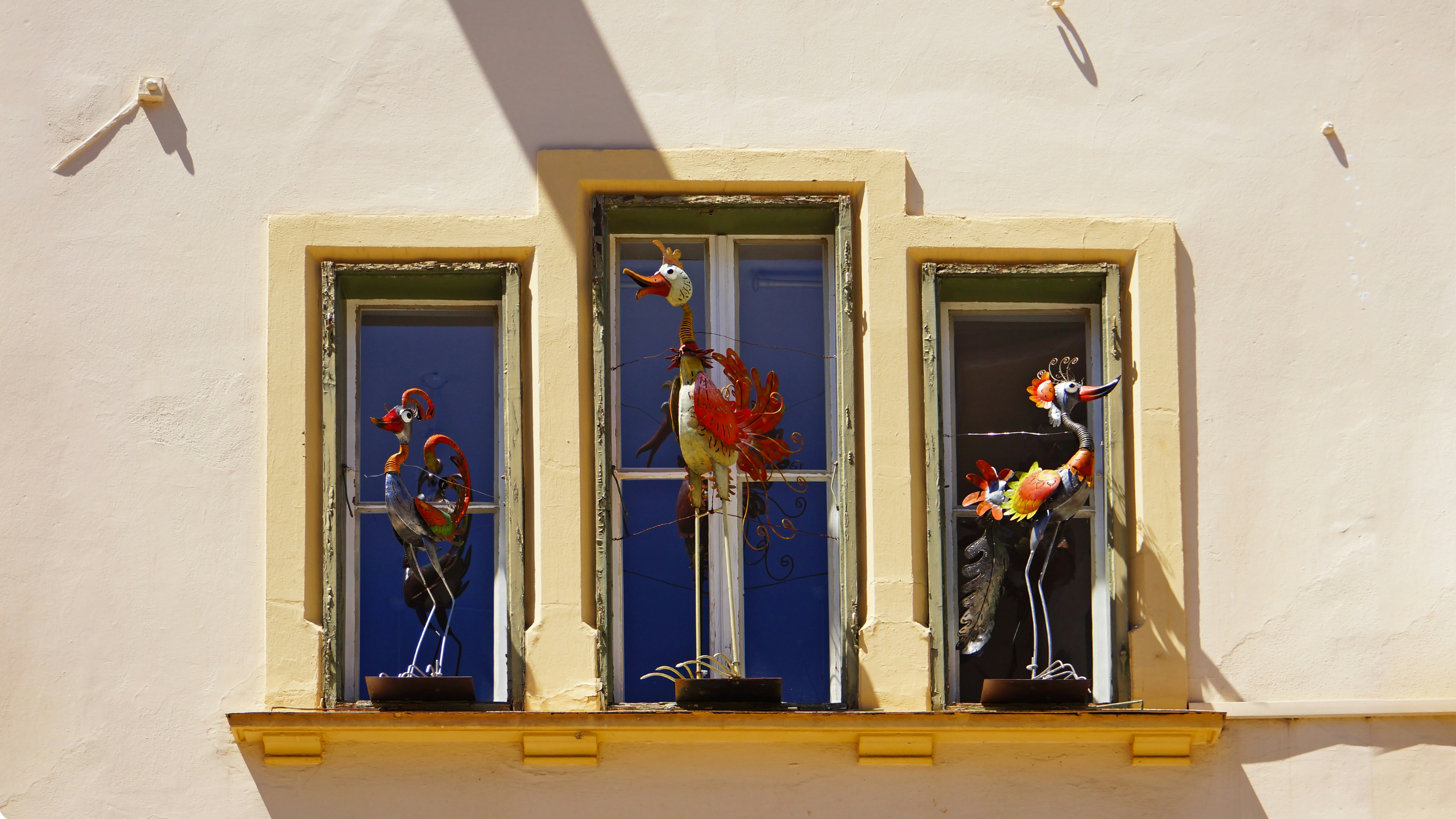 Colorful stilted birds guard a sunlit trio of windows