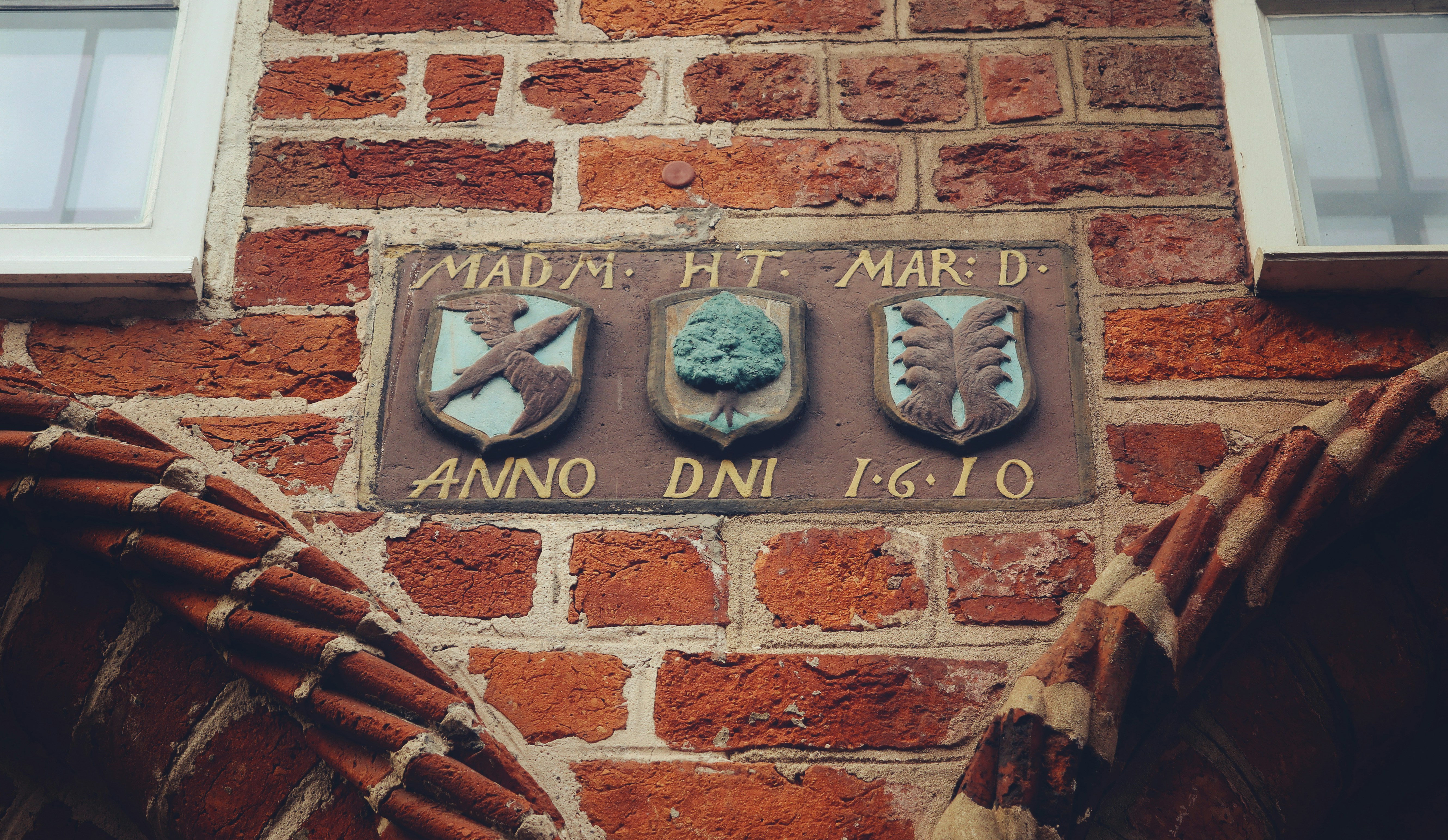 Historical plaque featuring three crests set against a rustic brick wall, inscribed with the year 1610.