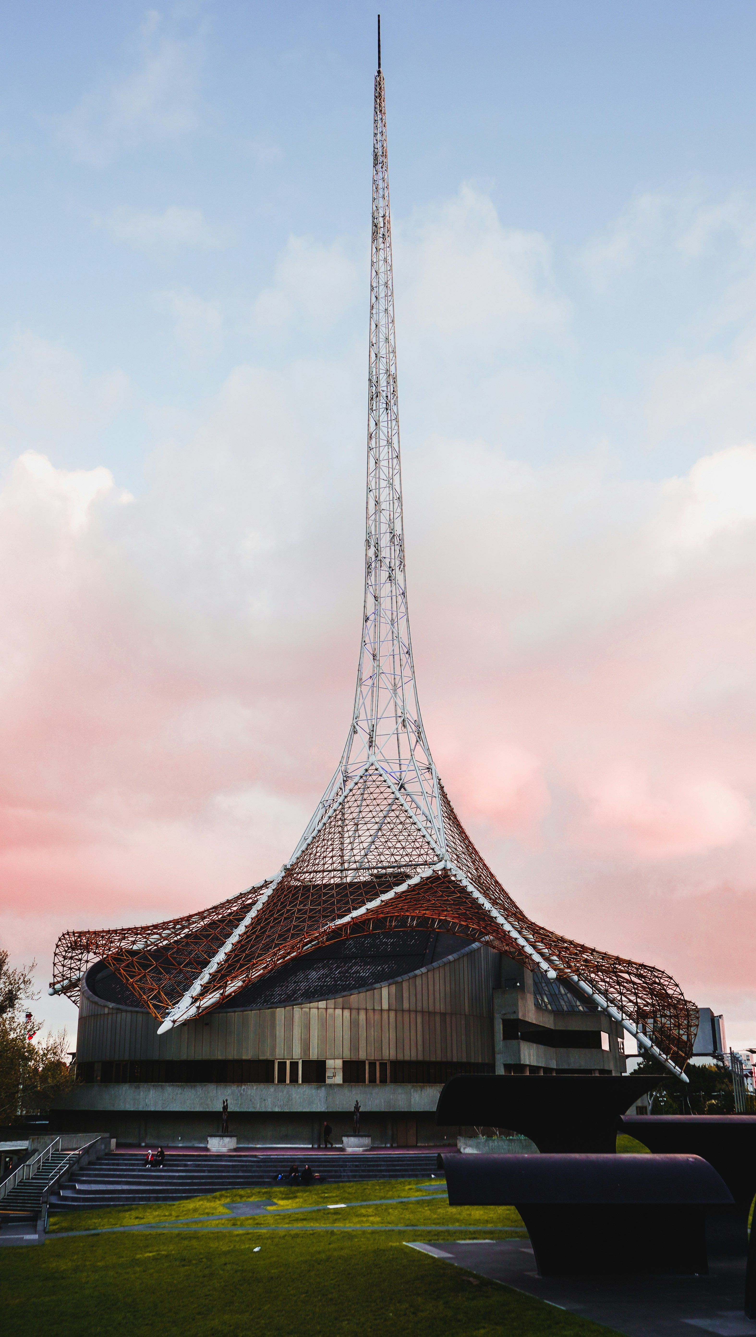 Spire of Steel: Lattice Tower Piercing a Sunset Over a Curved Roof