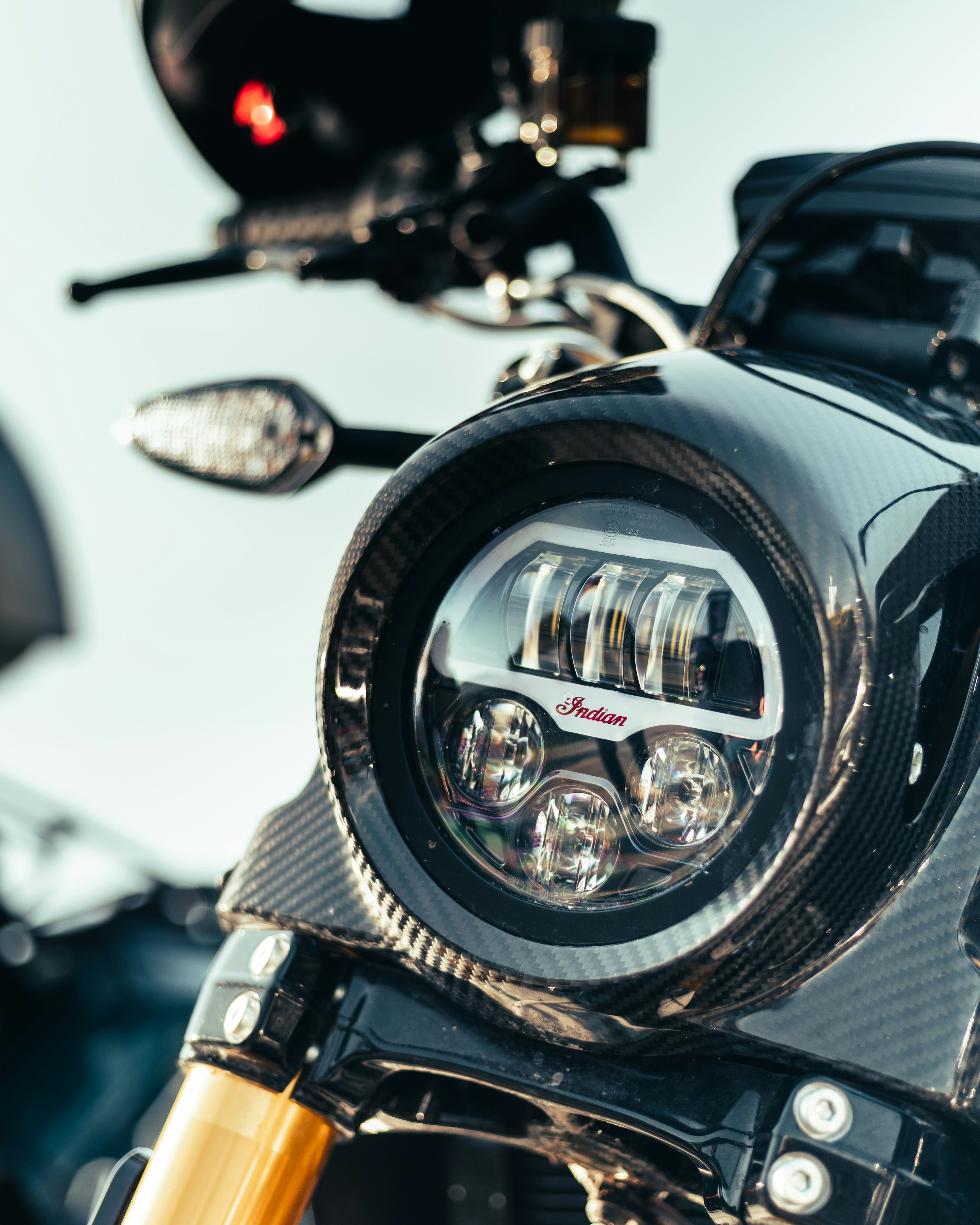 Close-up of a motorcycle's headlight with a carbon fiber finish and intricate details.