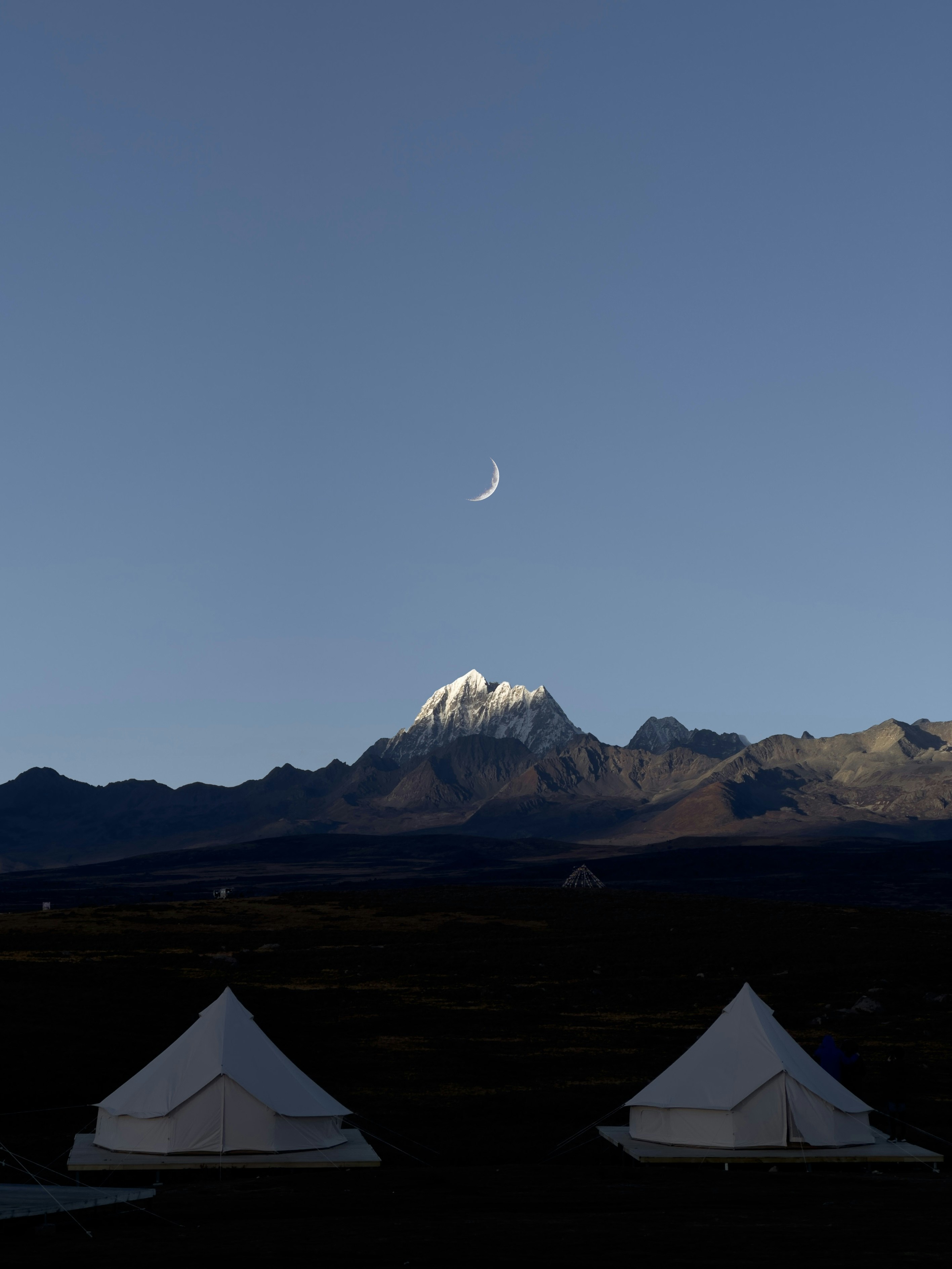 Crescent Moon Over a Snow-Capped Ridge and Tented Camp